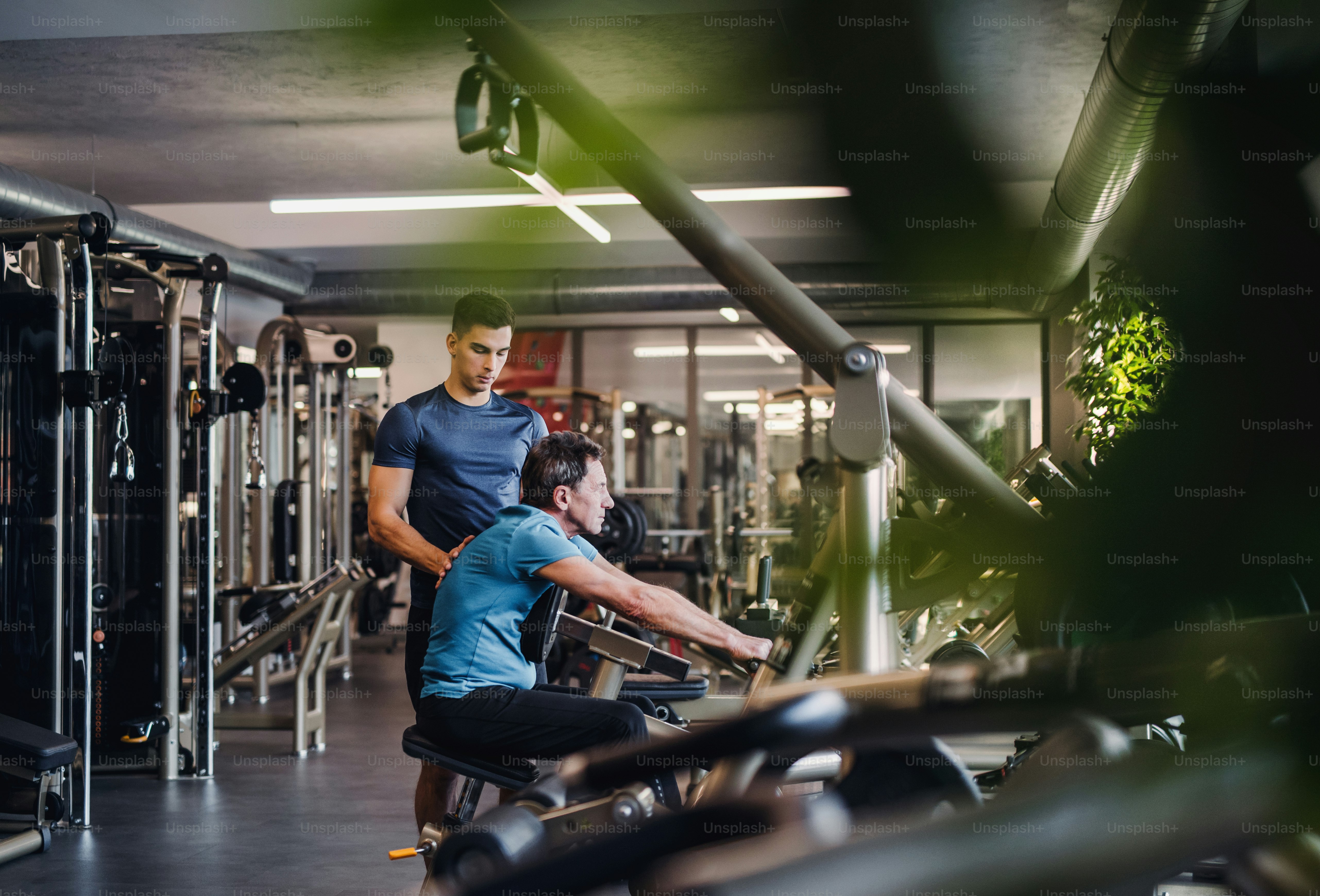 A senior man with a young male trainer doing strength workout exercise ...