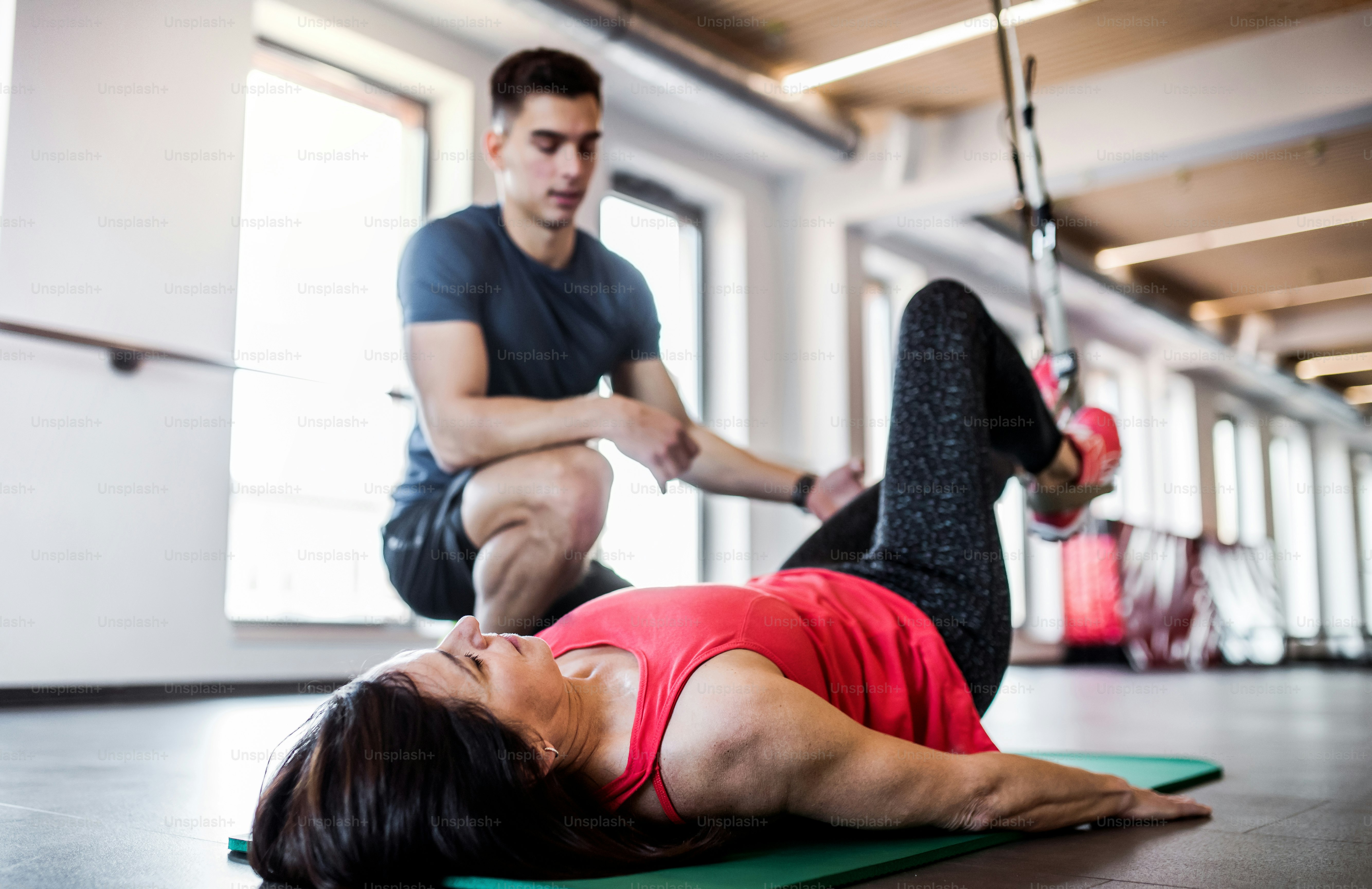 A senior man with a young male trainer doing strength workout exercise ...