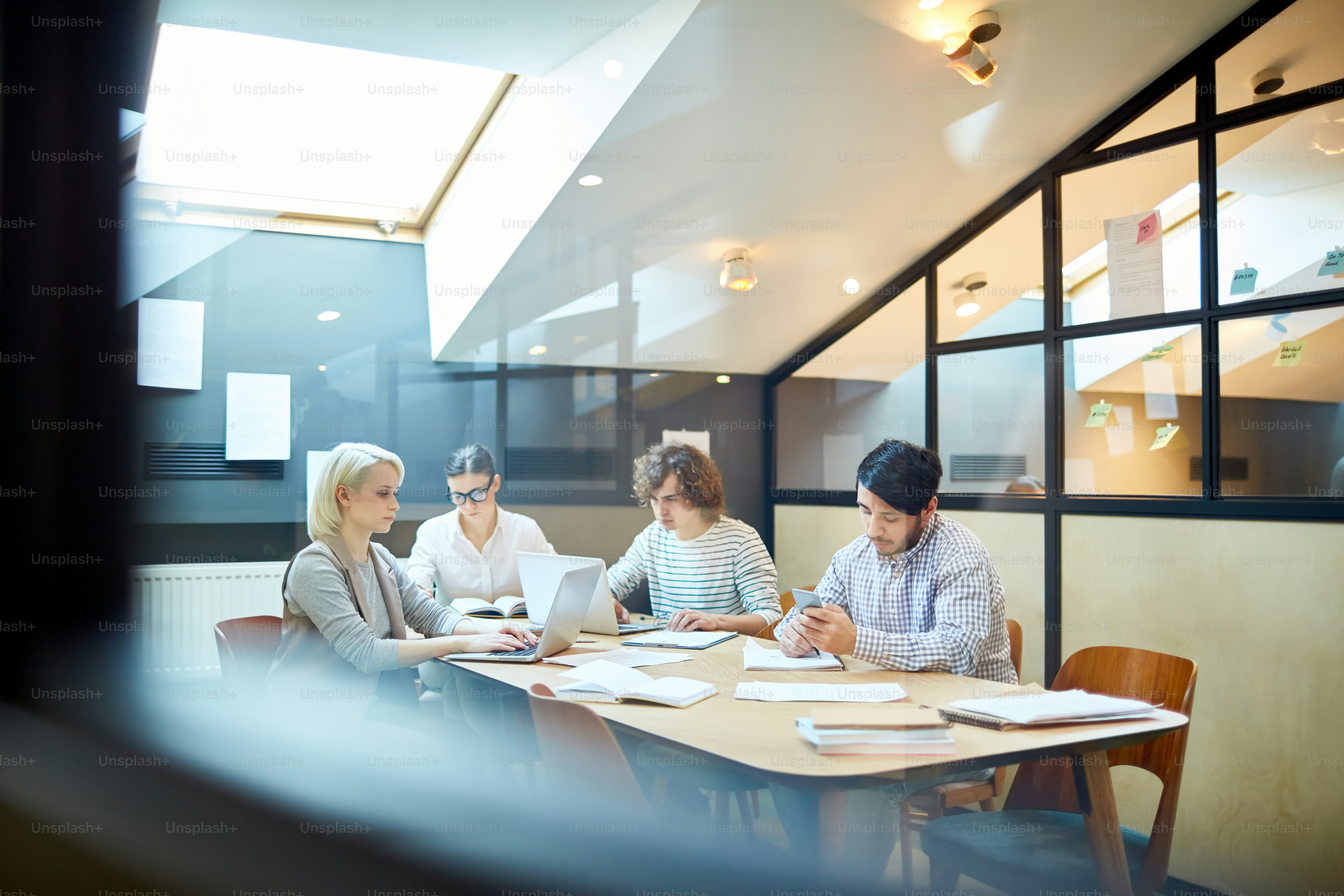 Four young contemporary managers sitting by one table and working individually photo – Russia ...