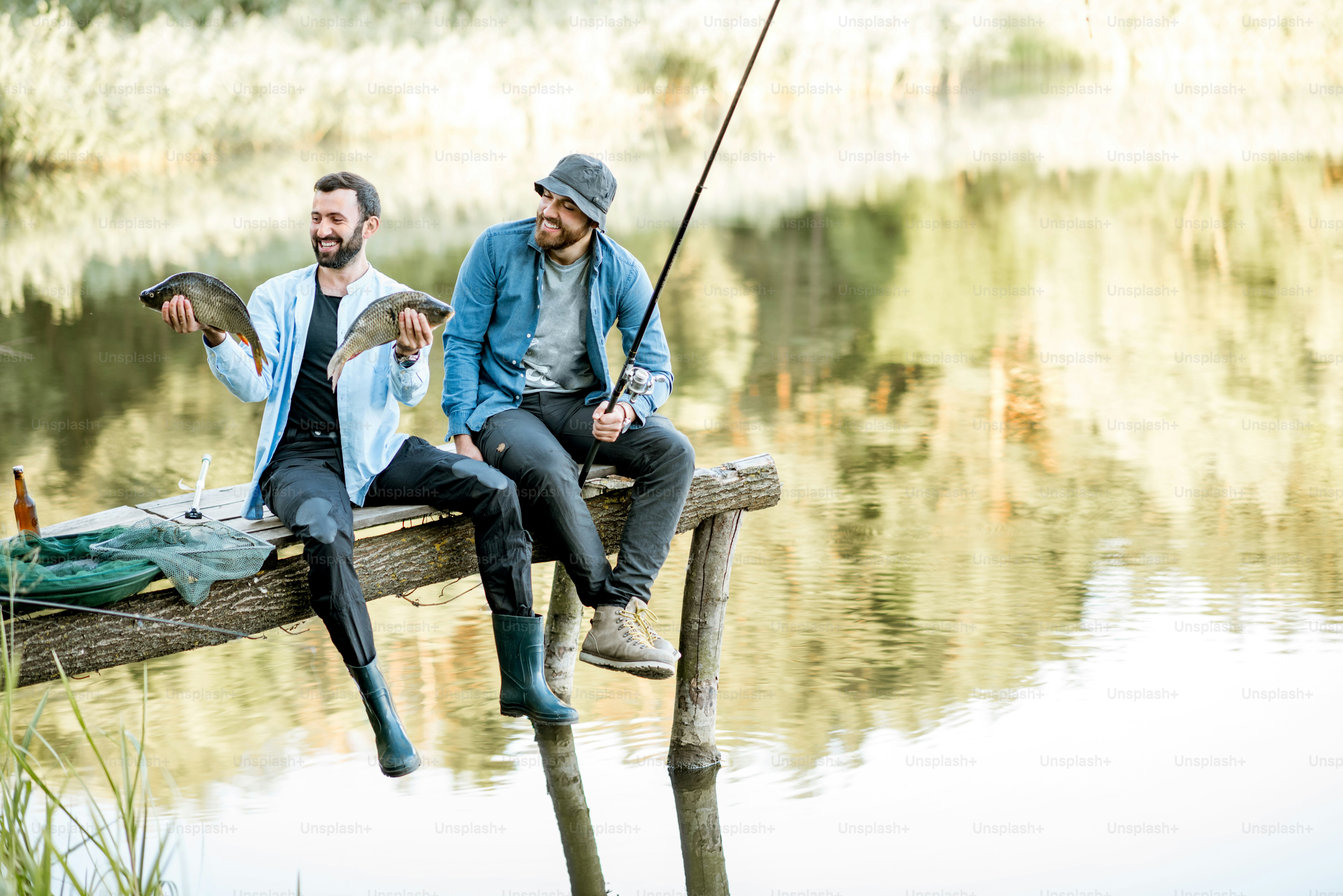 Deux pêcheurs heureux tenant des poissons pêchés assis sur la jetée en ...