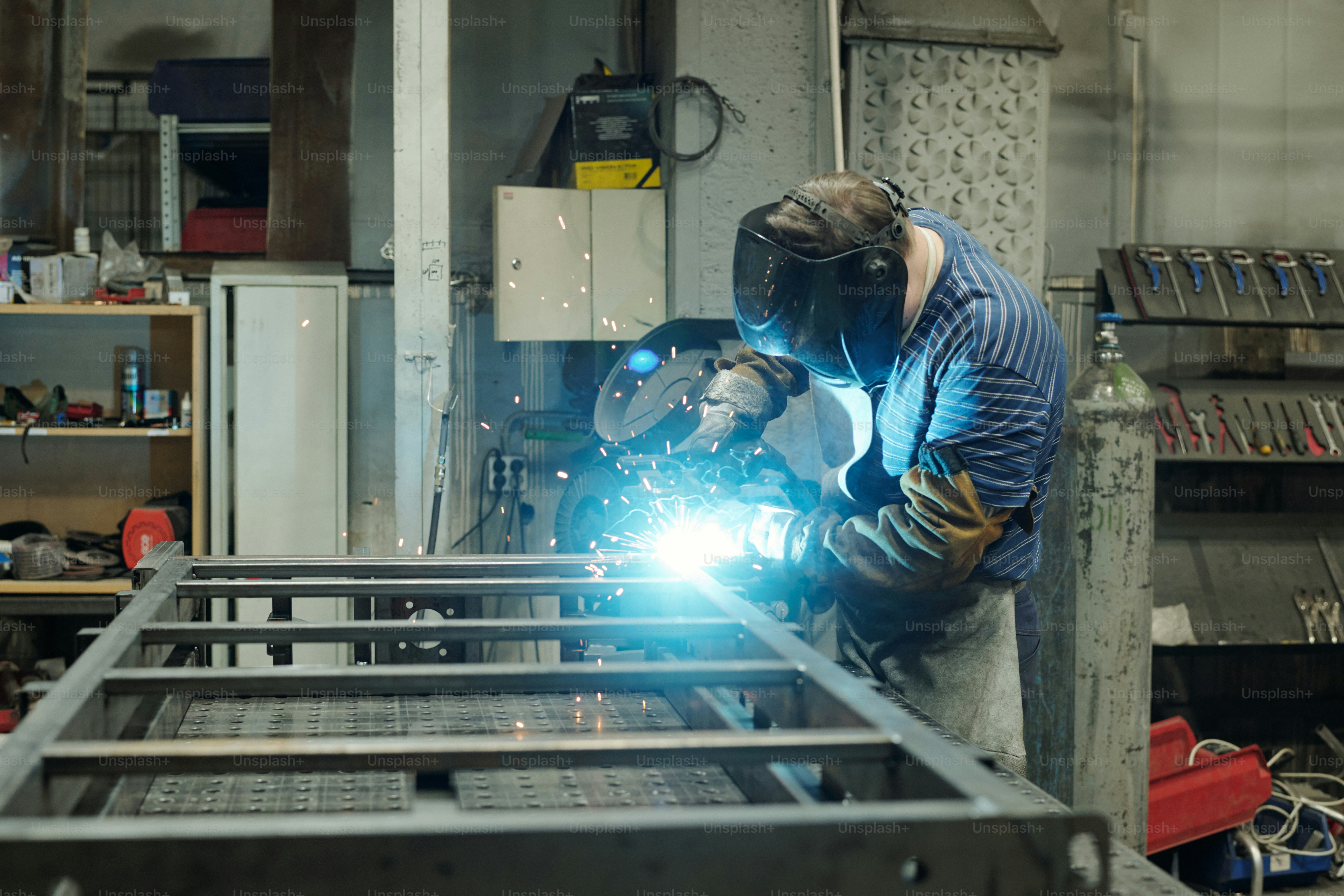 Side view of young male welder in protective face mask carrying out ...