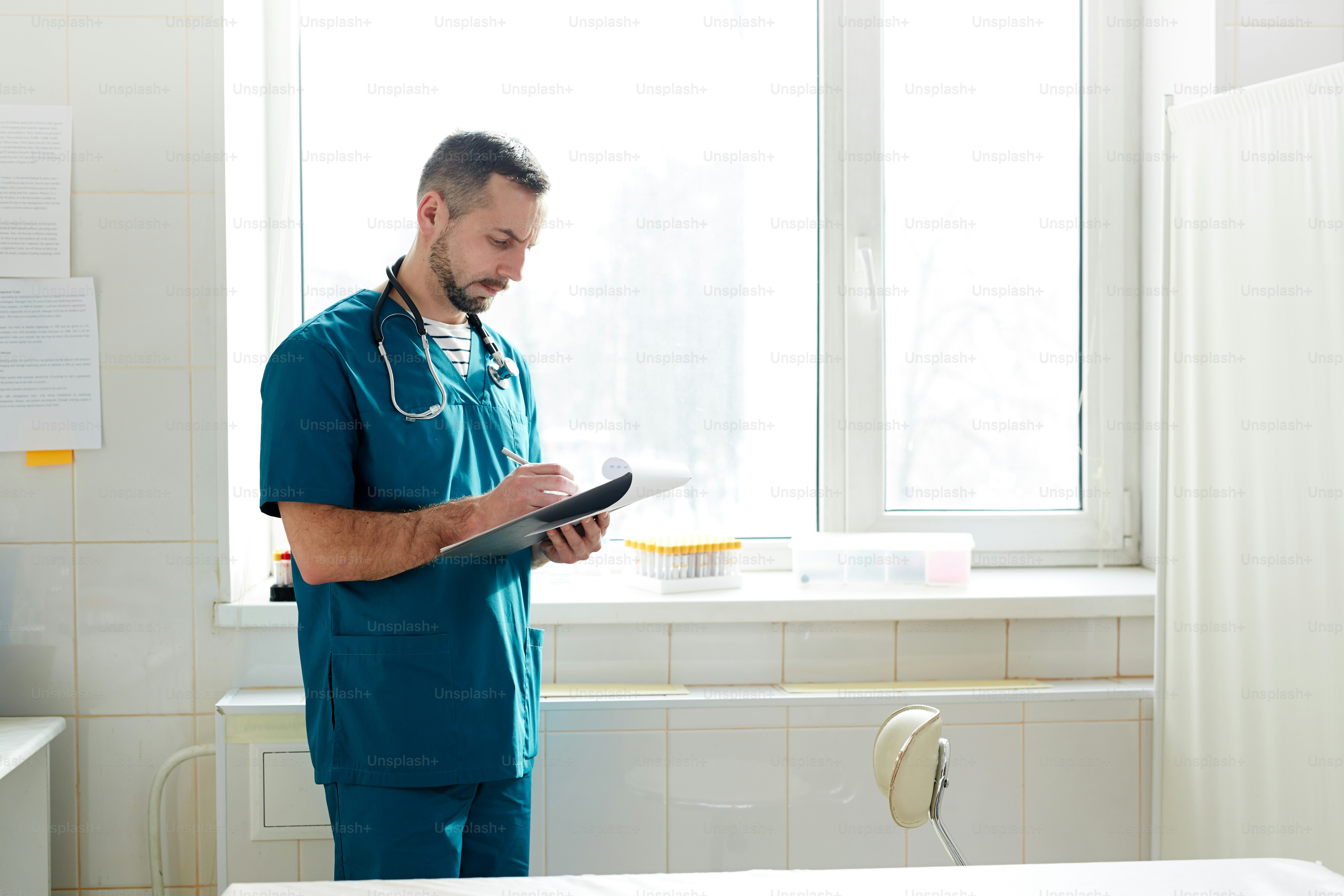 Young doctor in uniform making notes or prescription for patient in ...