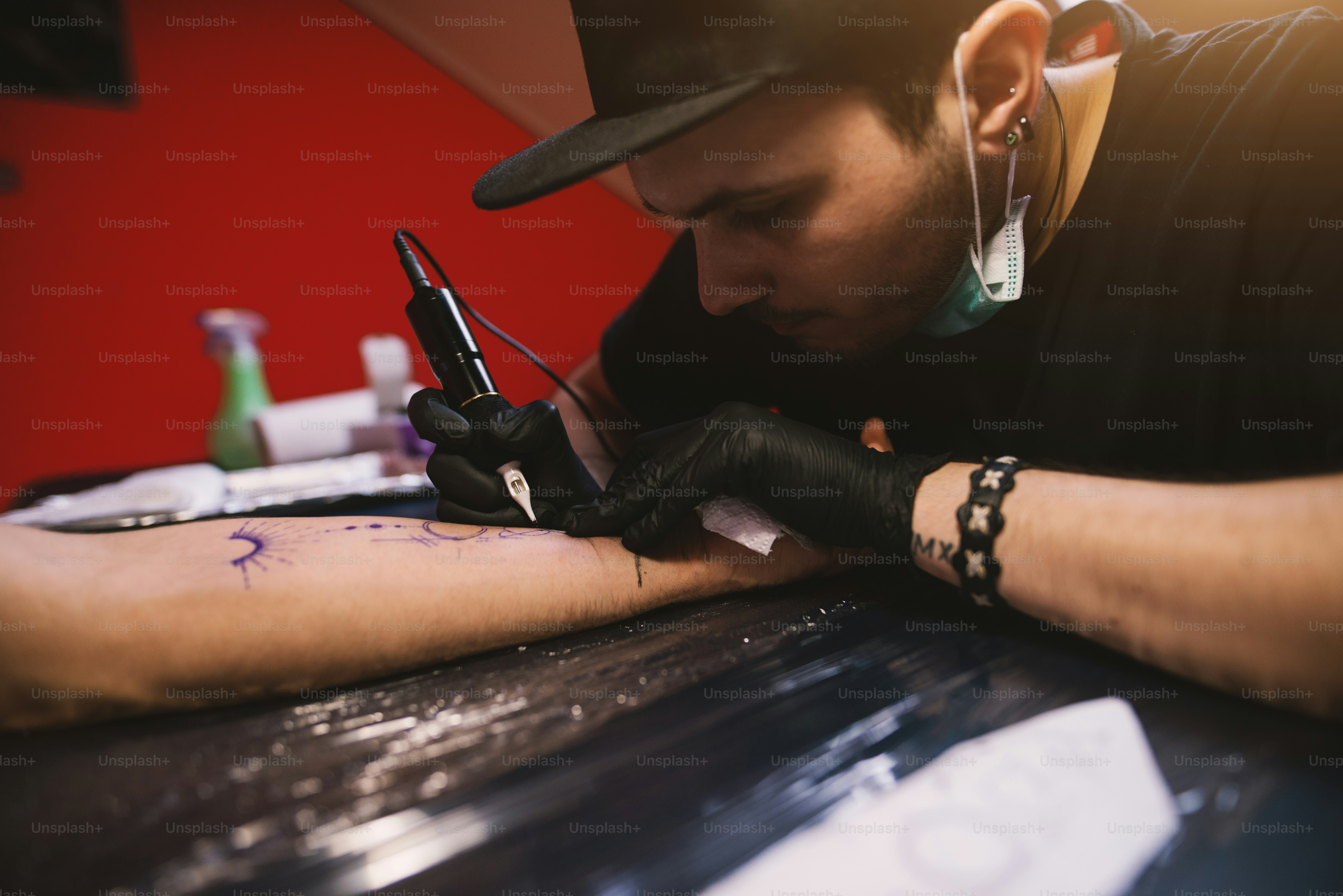Young focused tattoo artist is inking customers arm carefully in his ...