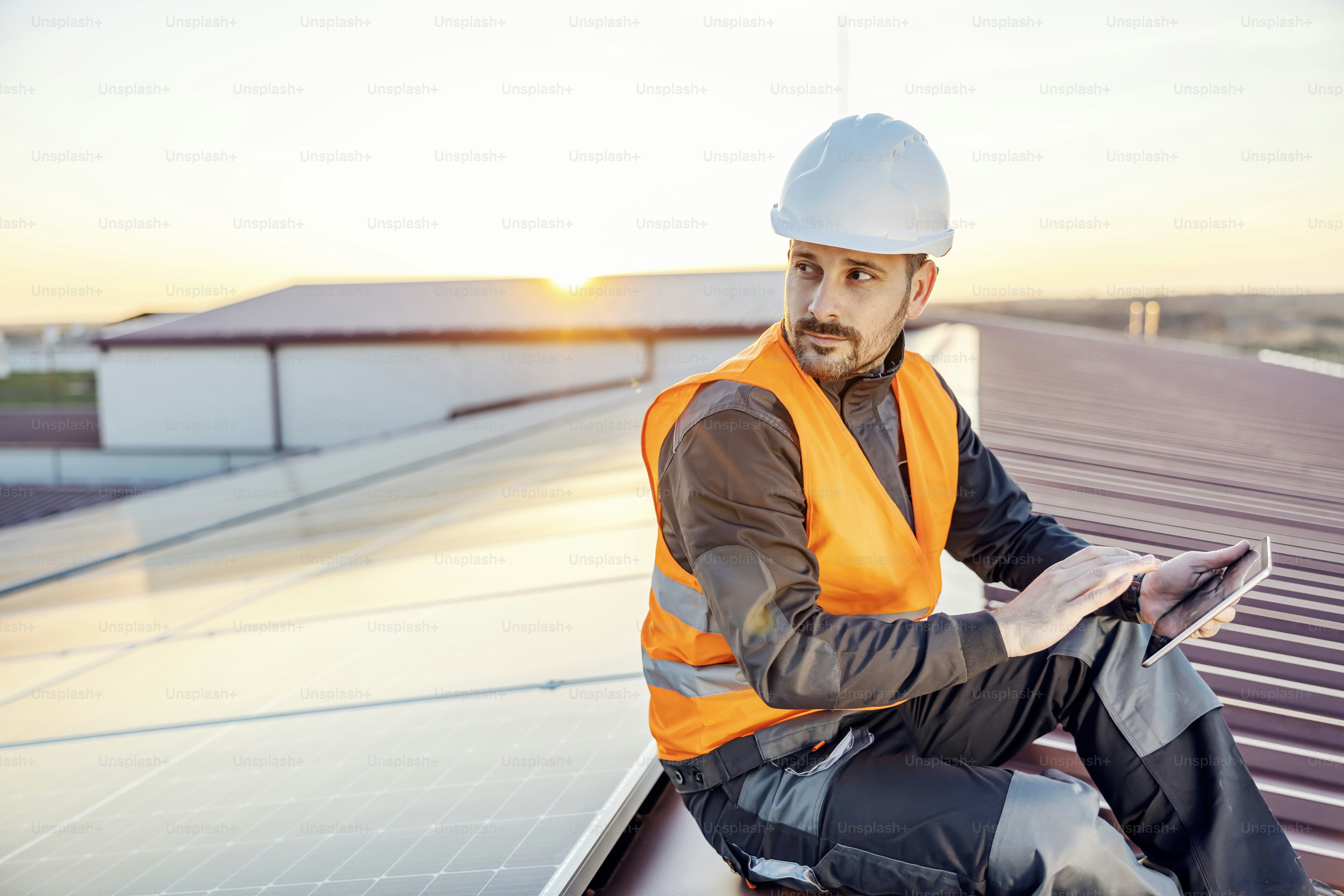 A supervisor sitting on the roof and holding pad to check on solar ...