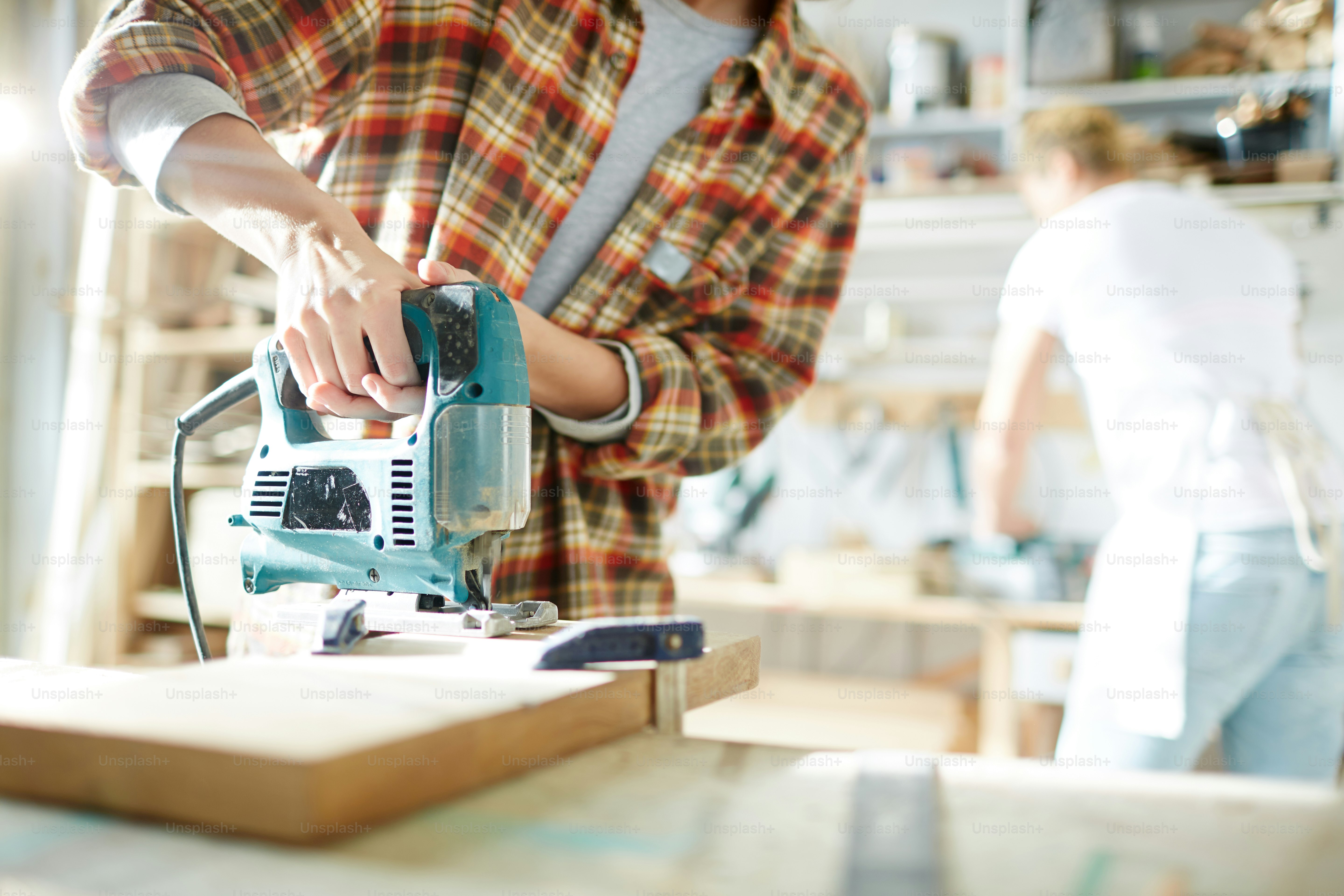 Hands of female worker with electric fretsaw working with wooden boards ...