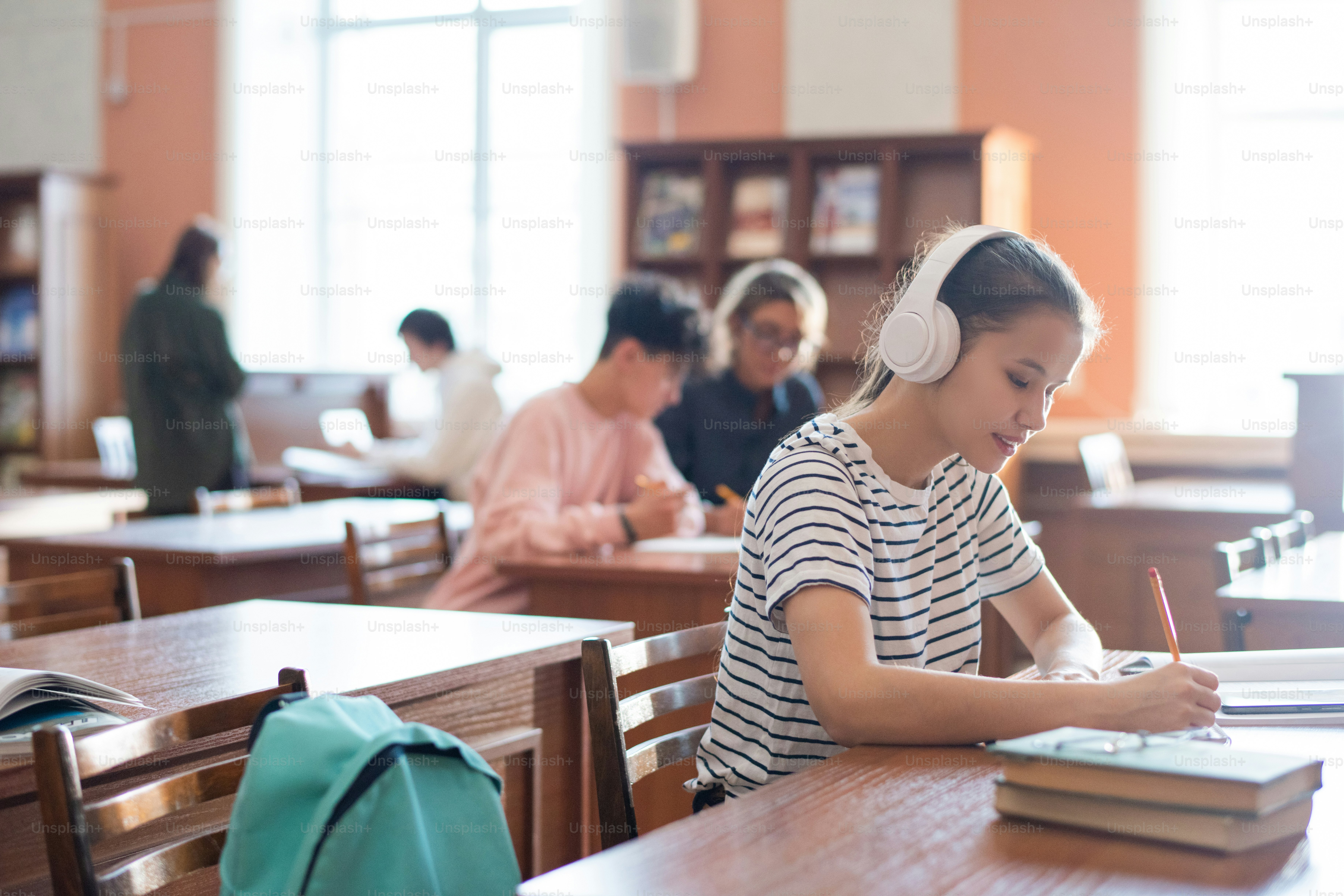 Group of contemporary college learners sitting by desks in library and ...