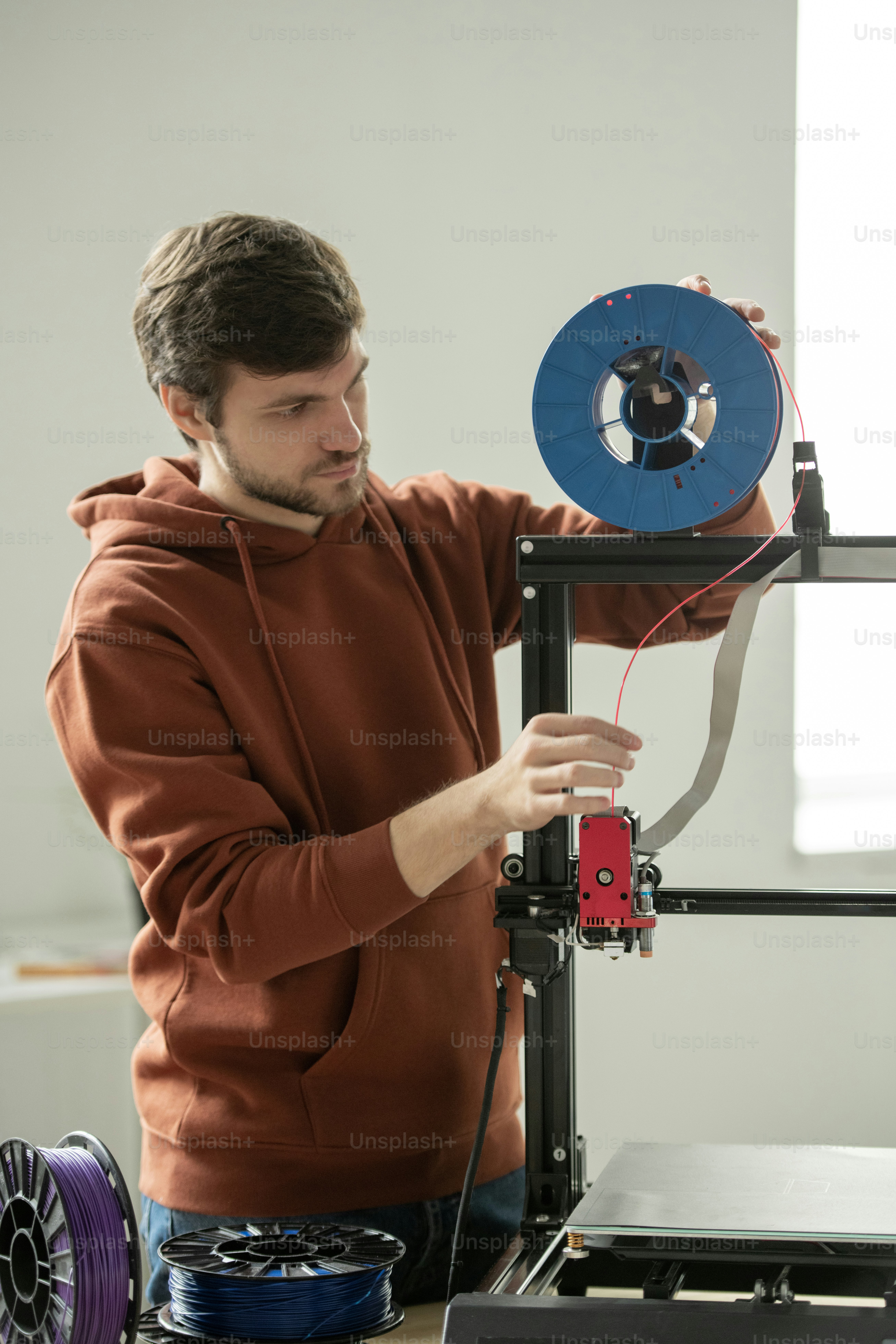 Young man in casualwear putting red filament into printhead of 3d ...