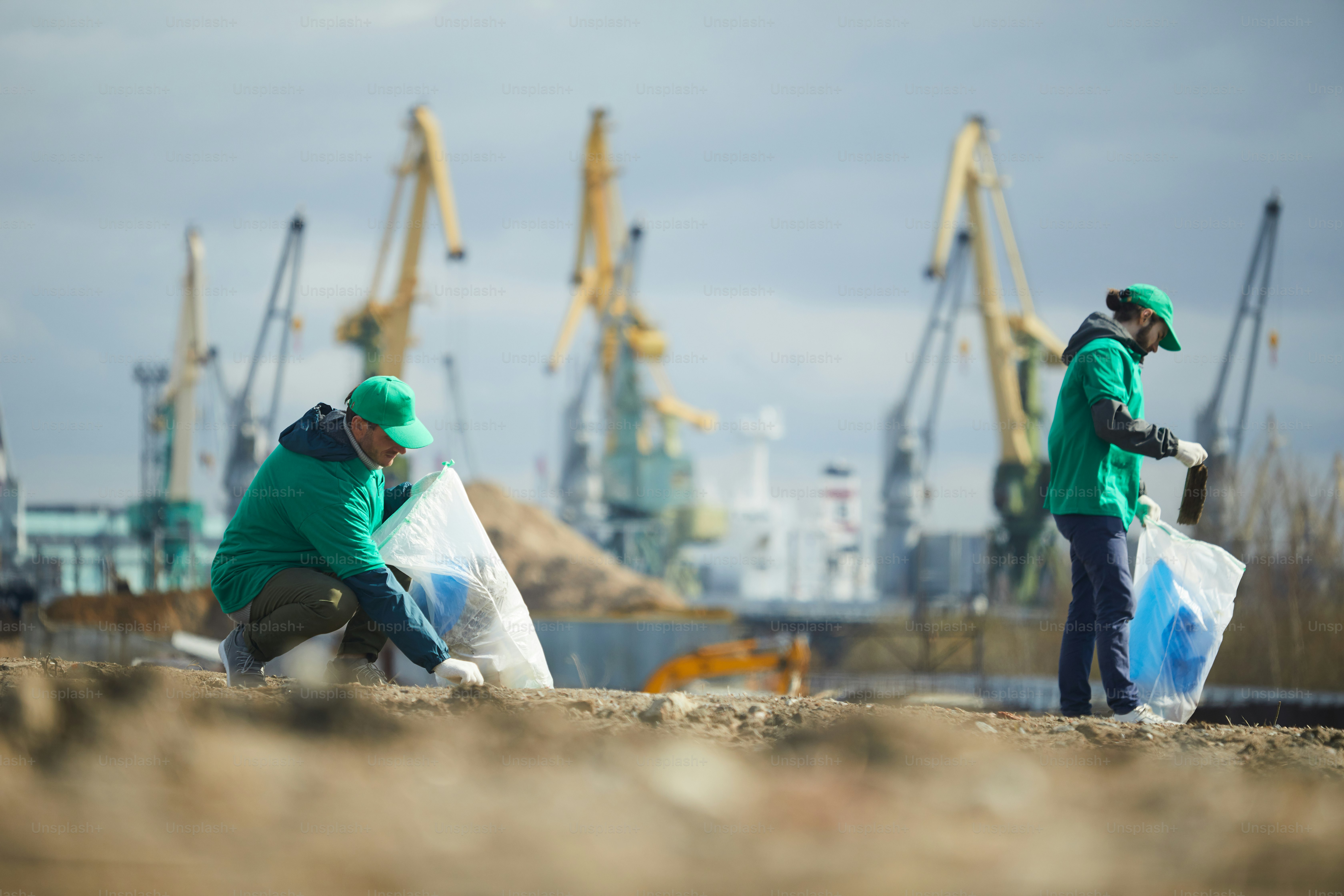 Two young men in uniform putting litter and garbage into big sacks ...