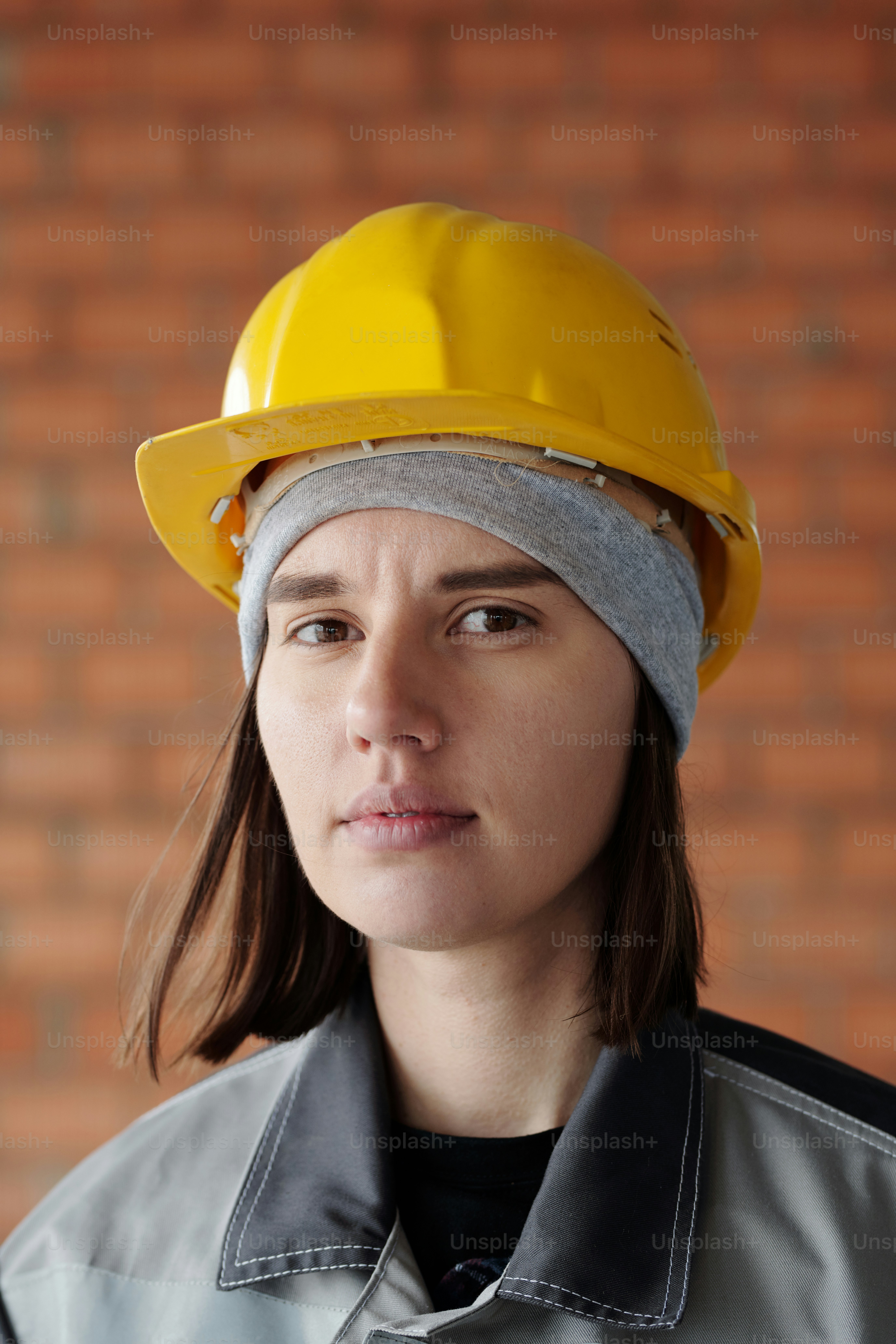 Young serious female builder in protective helmet and workear taking ...