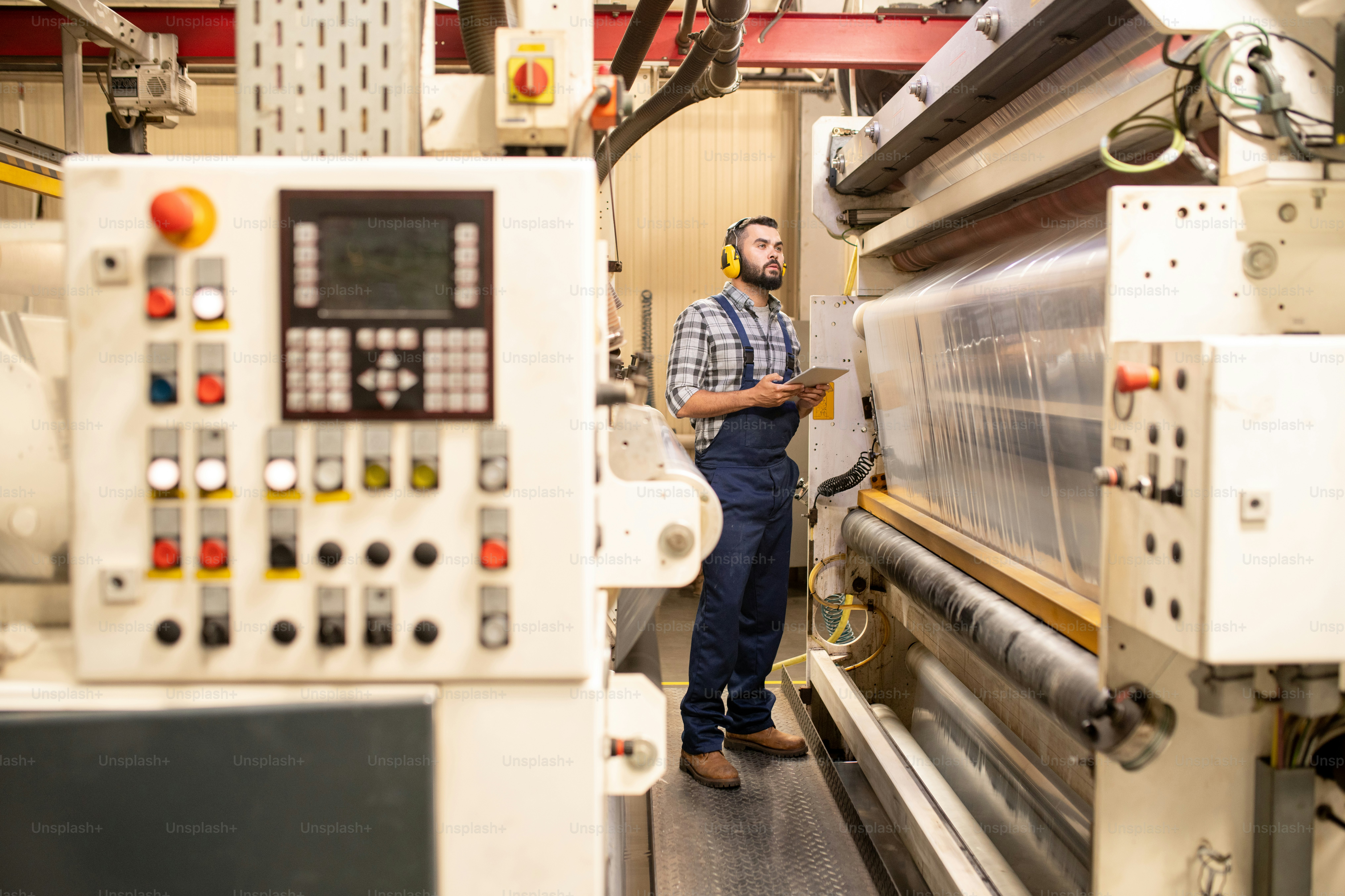 Young factory engineer in workwear standing by processing line while ...