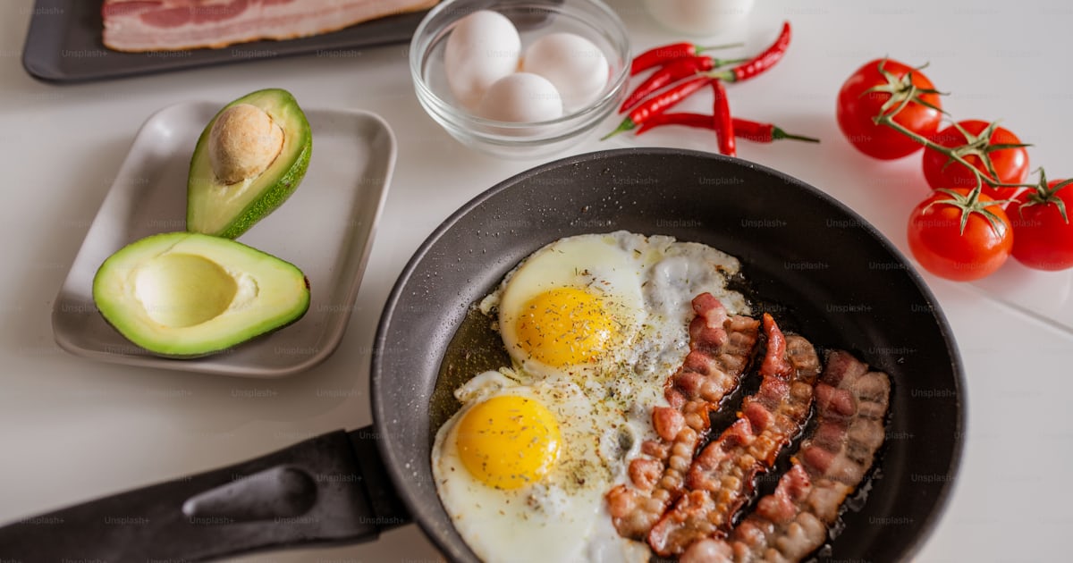계란 후라이와 향신료를 뿌린 베이컨 신선한 아보카도 붉은 익은 토마토 매운 칠리 페퍼를 식탁에 뿌린 프라이팬 사진