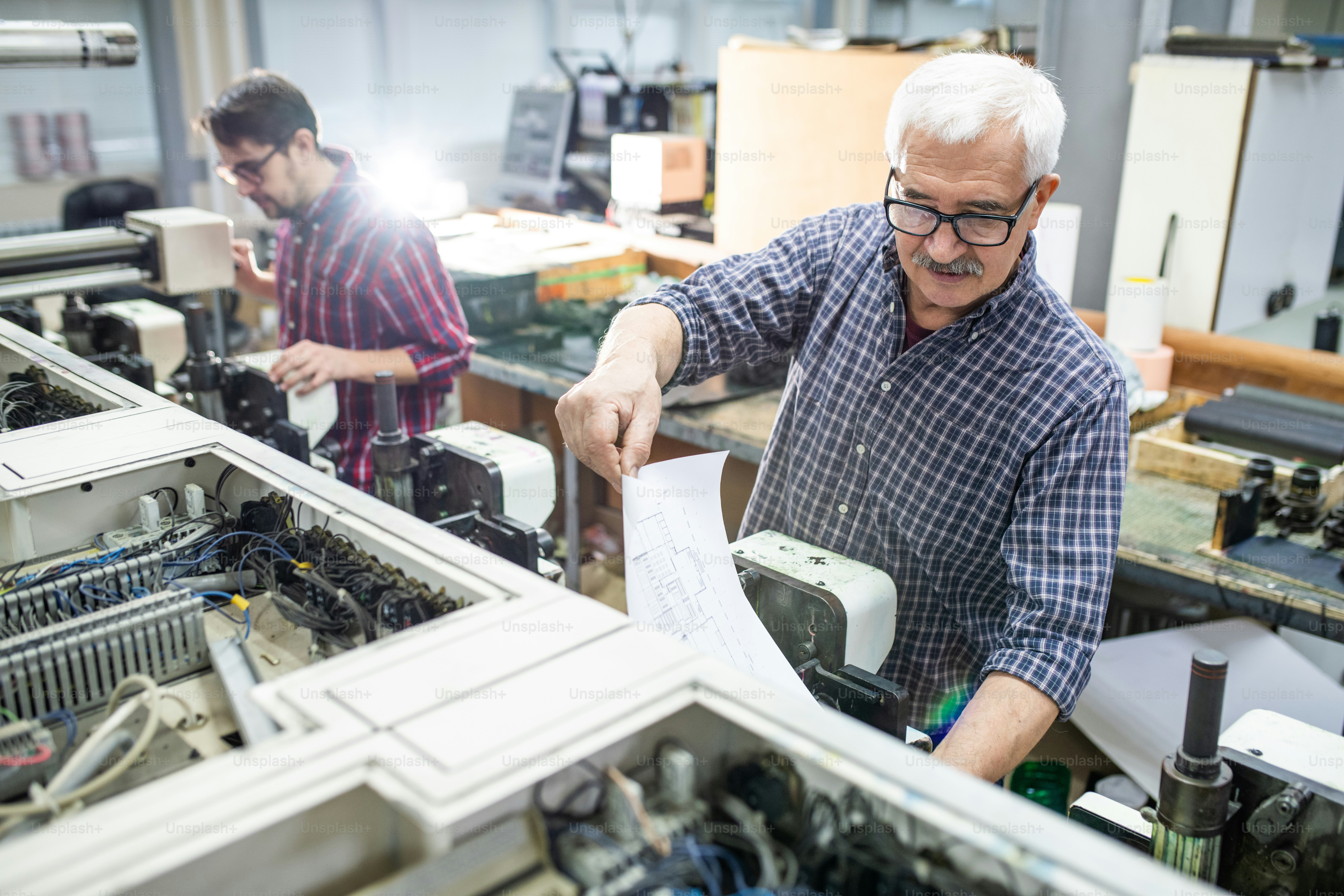 Busy senior man in glasses getting paper out of large printer in ...