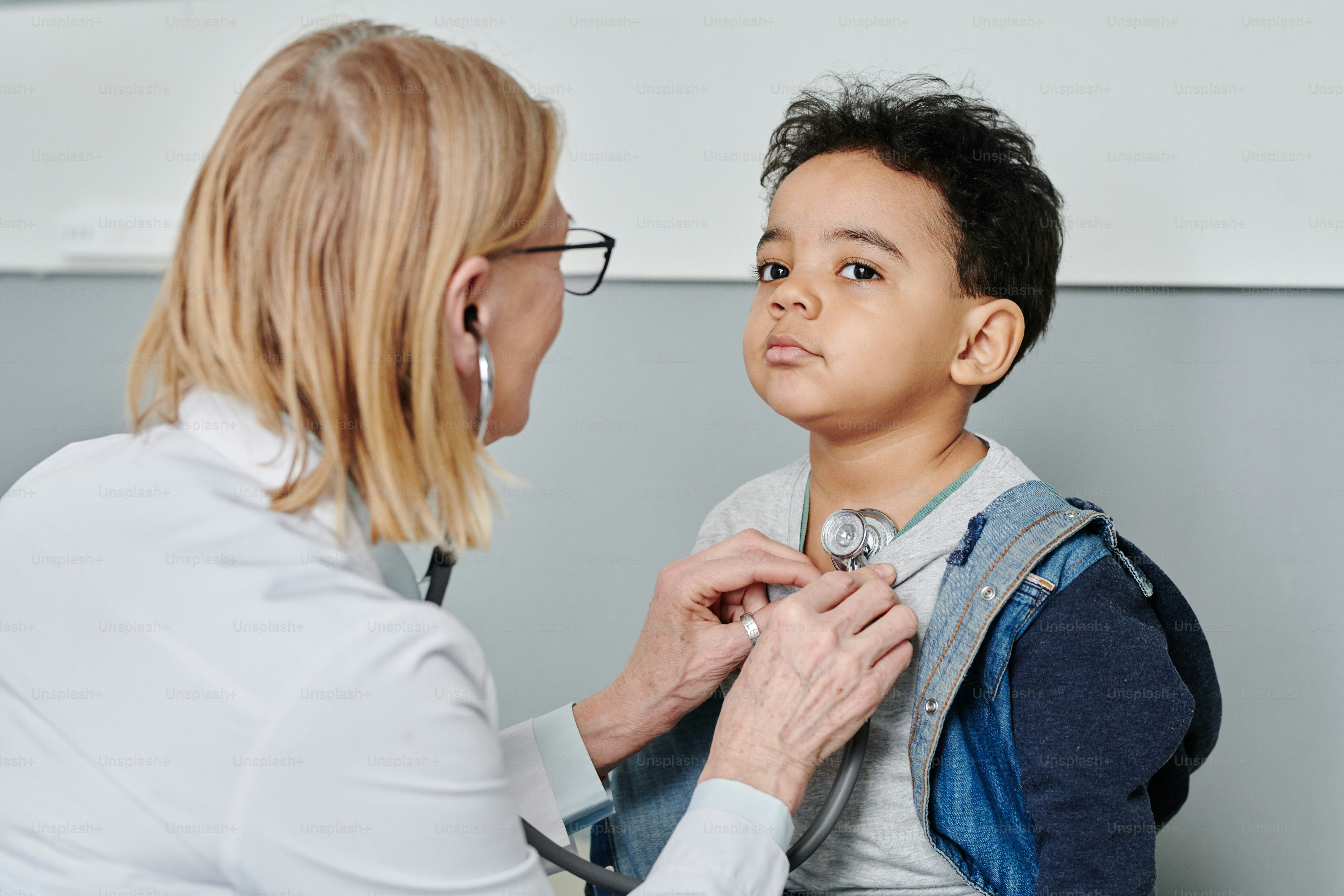 Cute sick little boy in casualwear sitting by wall of medical office ...