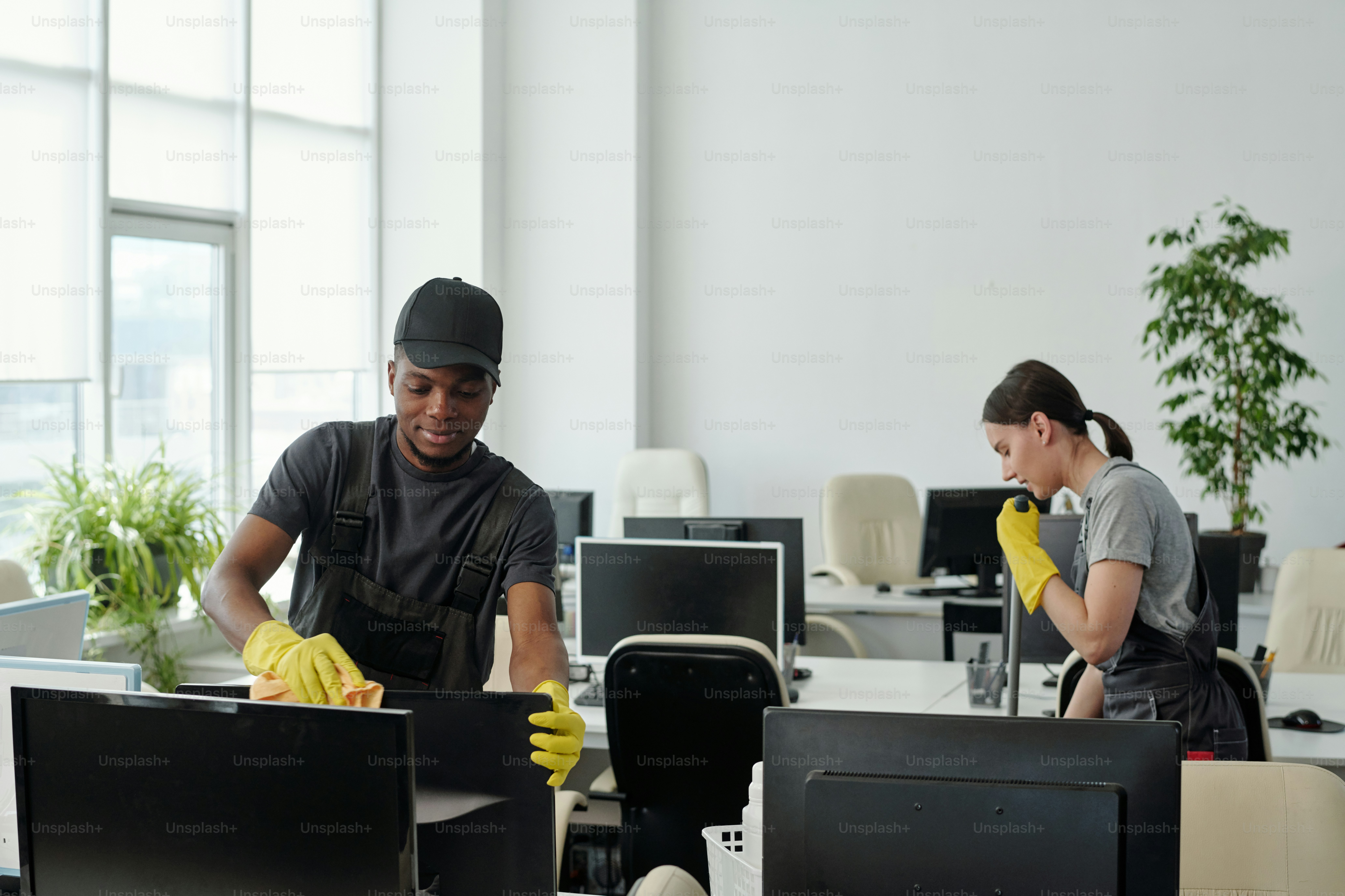Young male staff of modern cleaning service company wiping computer ...