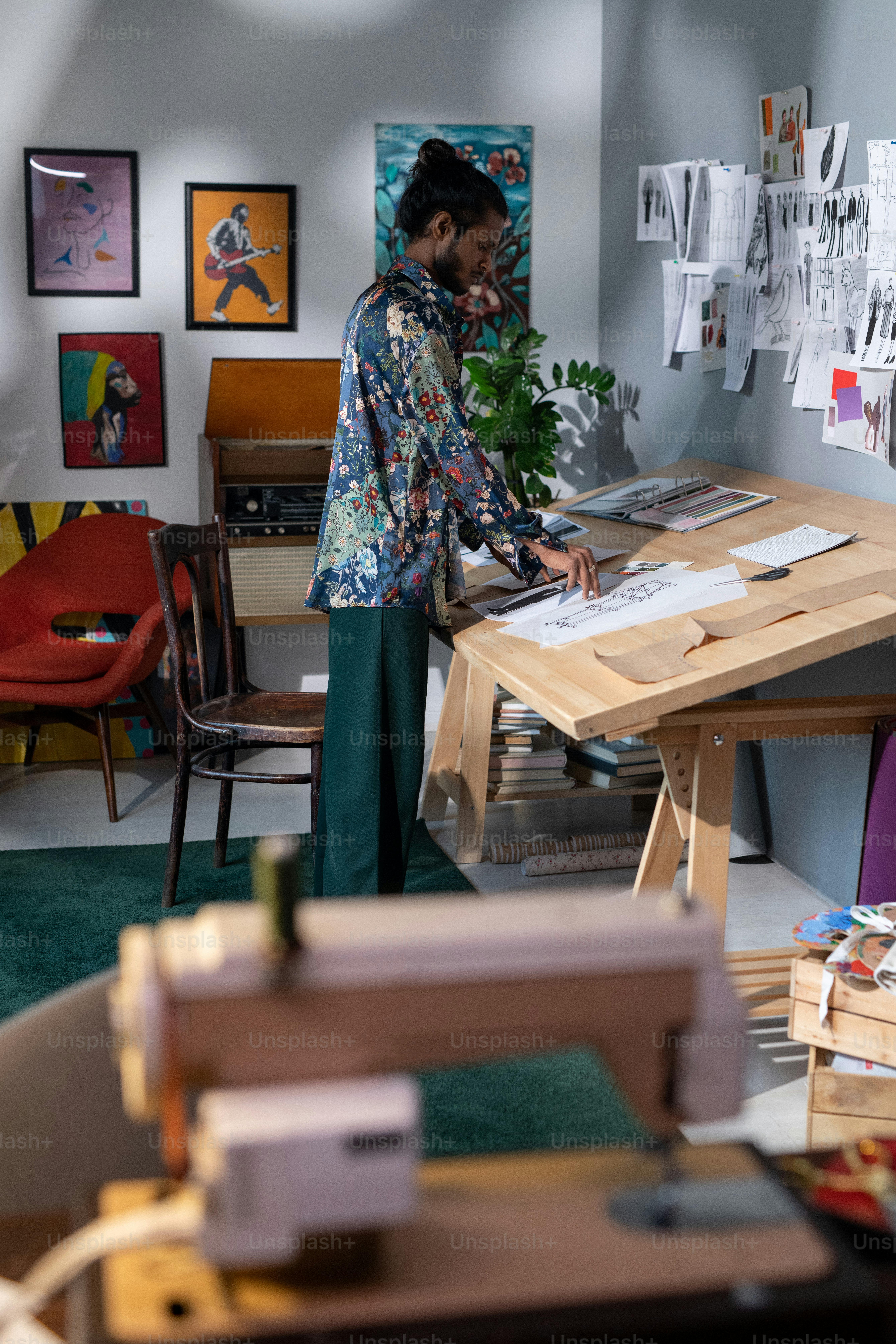 Young creative man standing by wooden table with his artworks and ...