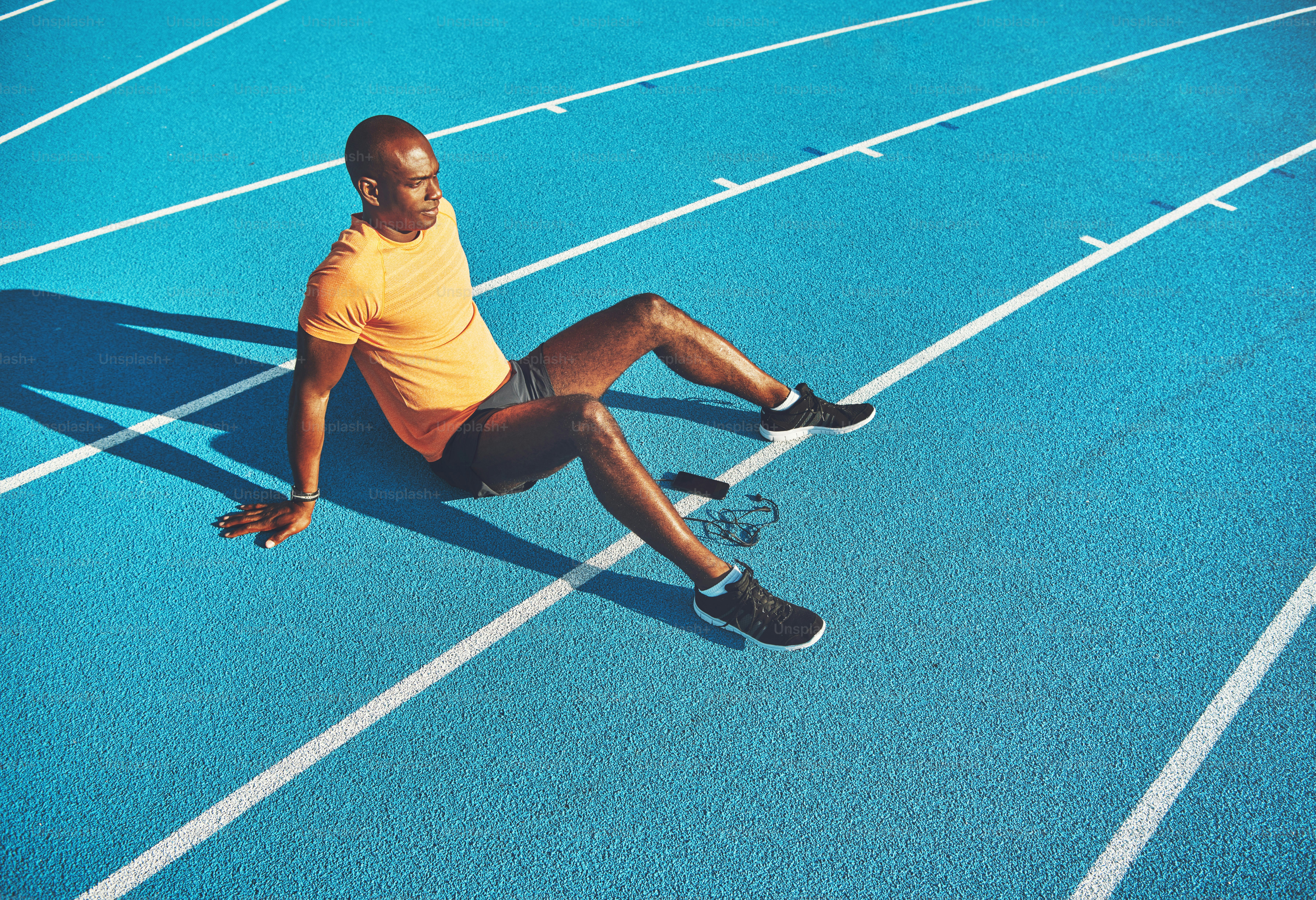 Fit young African runner sitting alone with his cellphone on a track ...