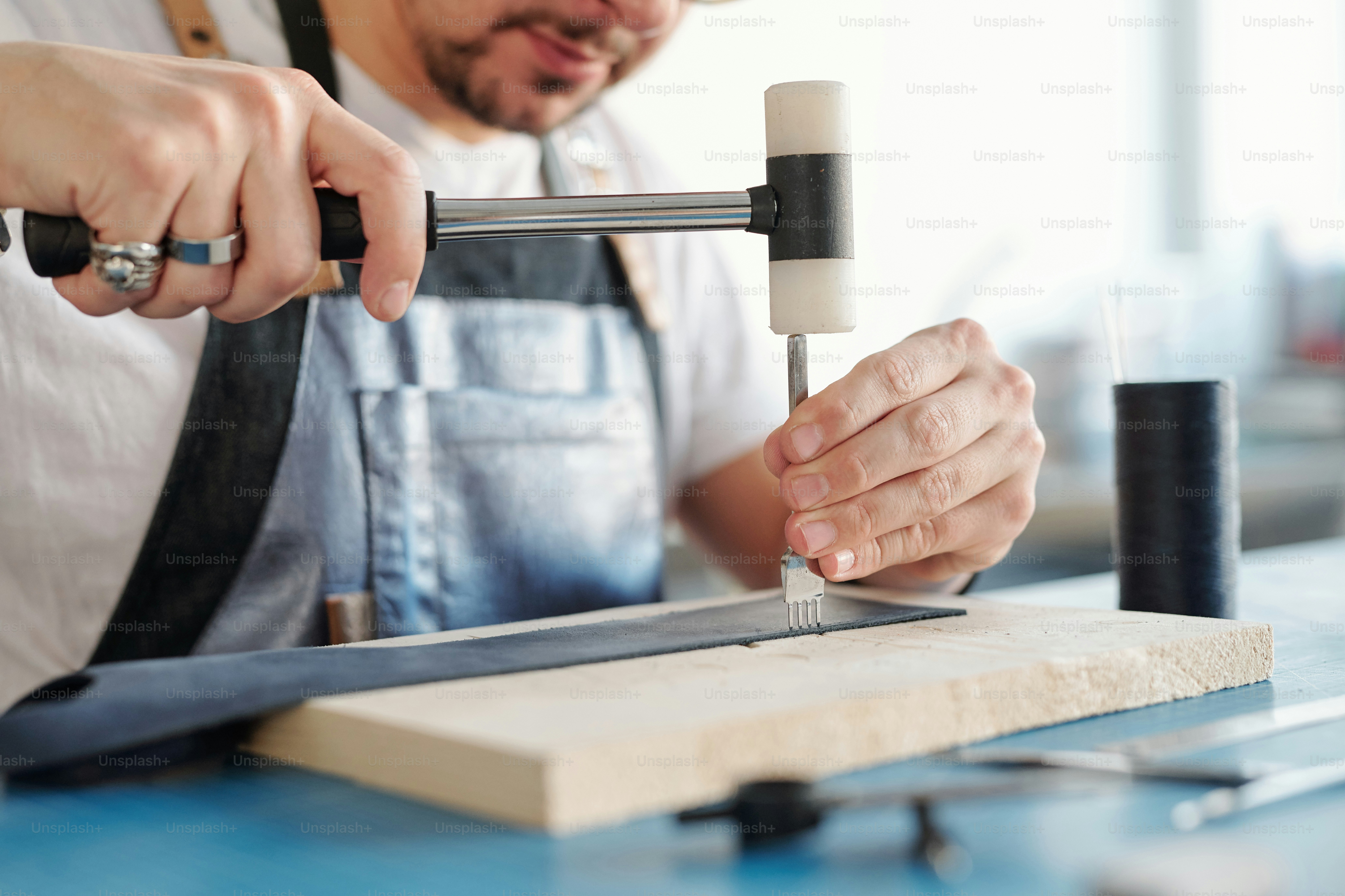 Close-up of skilled artisan hitting stitching chisel with hammer while ...