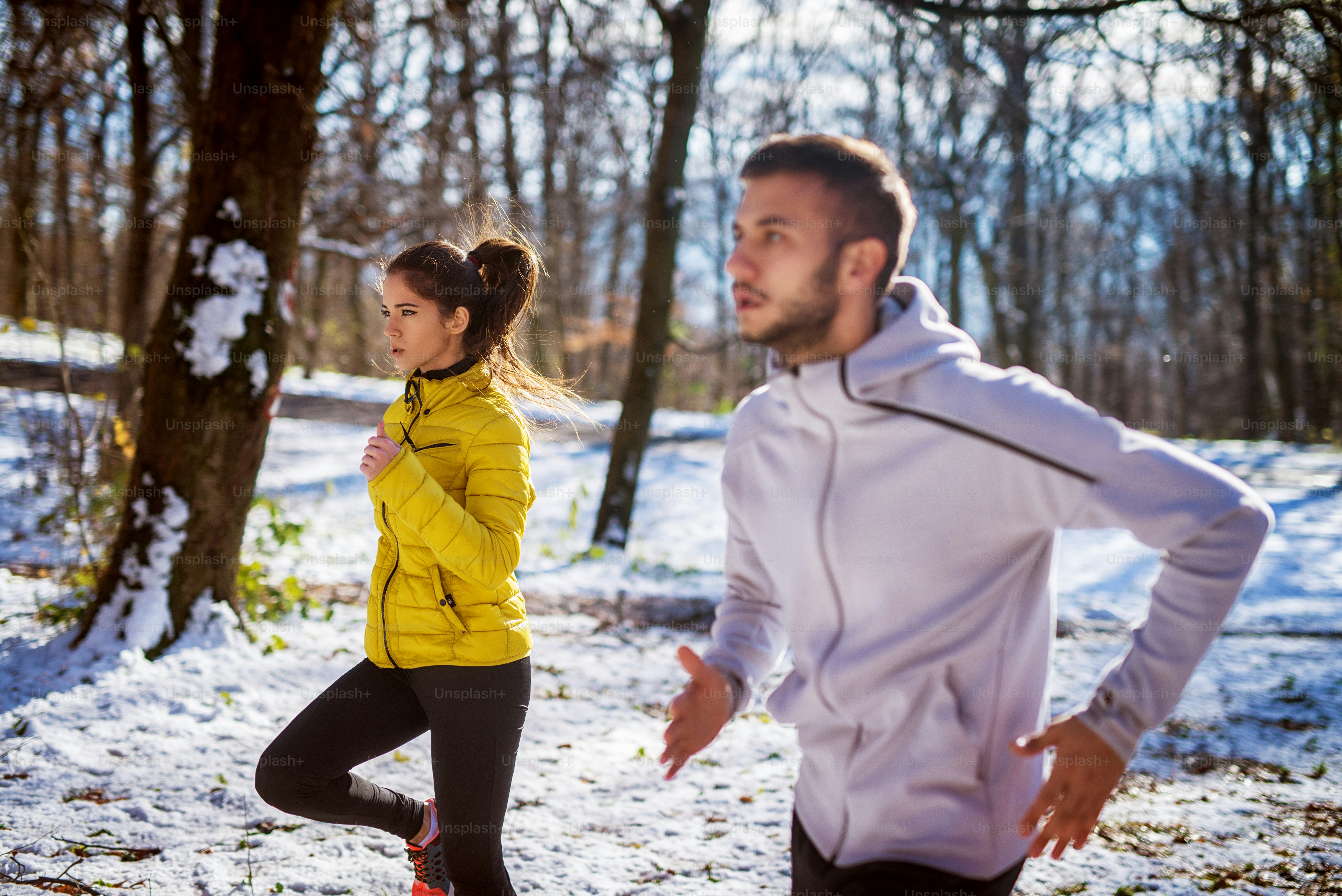 Focused strong active couple jogging in sportswear through the forest ...
