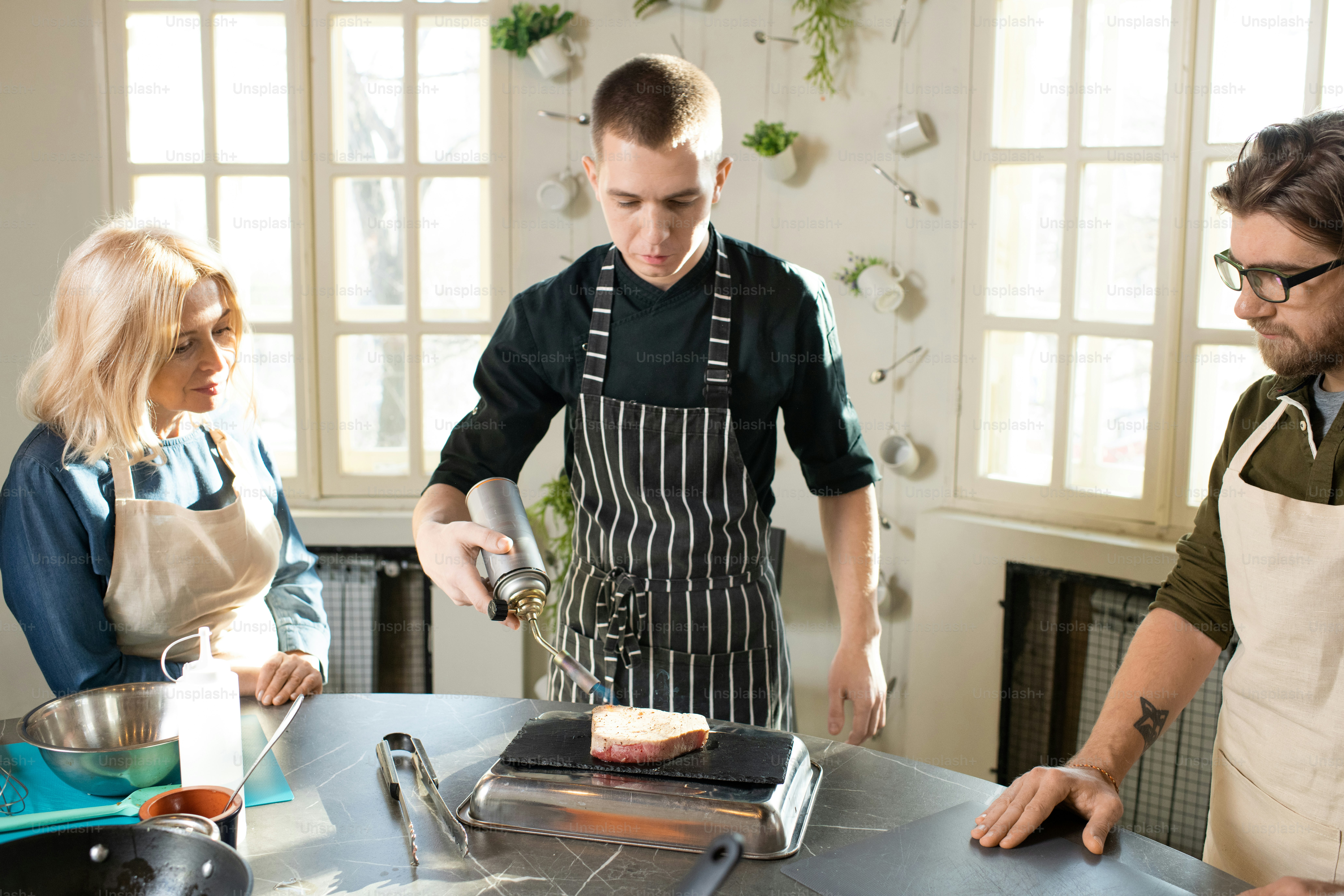 Young confident male coach in apron smoking piece of beef on special ...