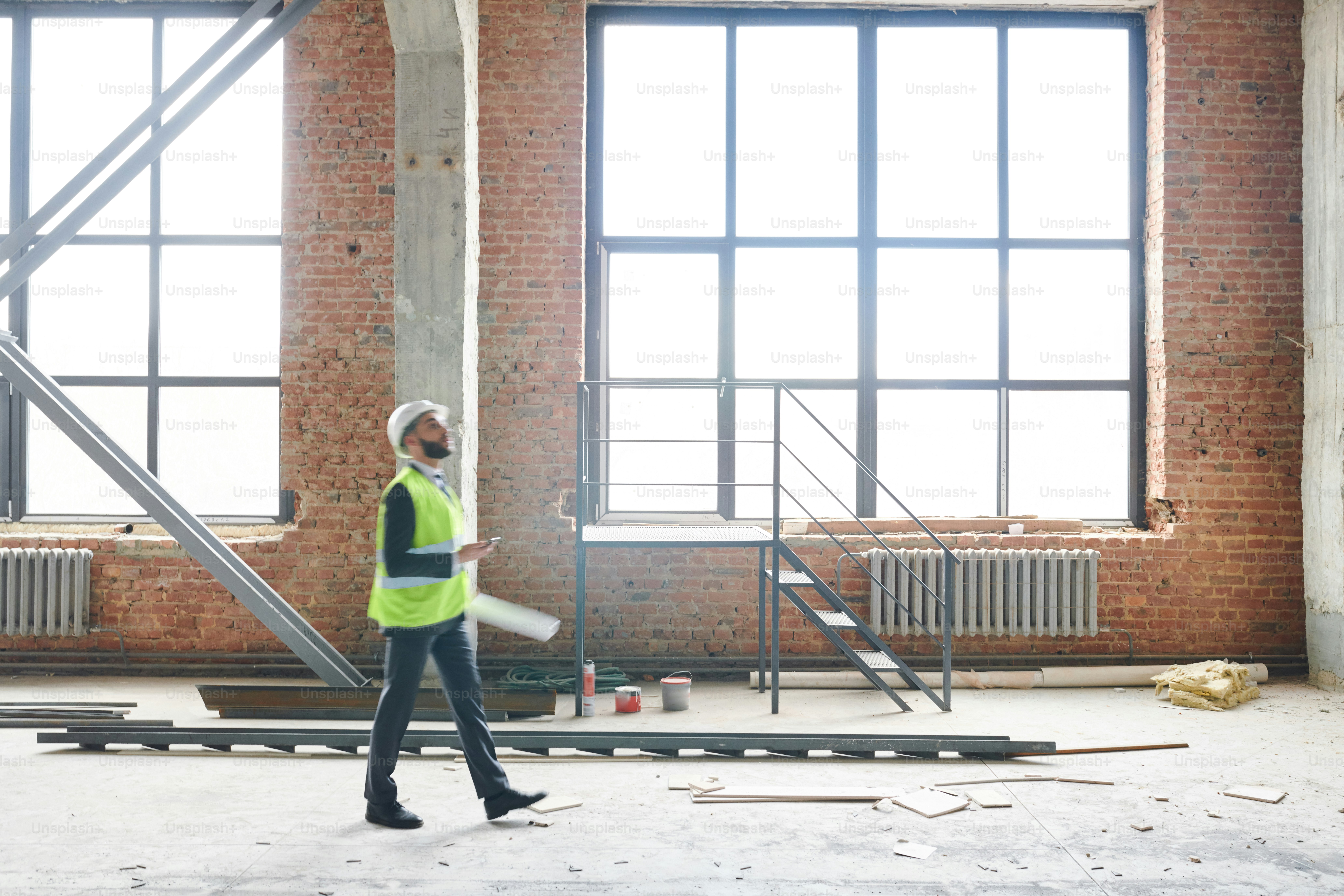 Young foreman in uniform walking inside unfinished construction while ...