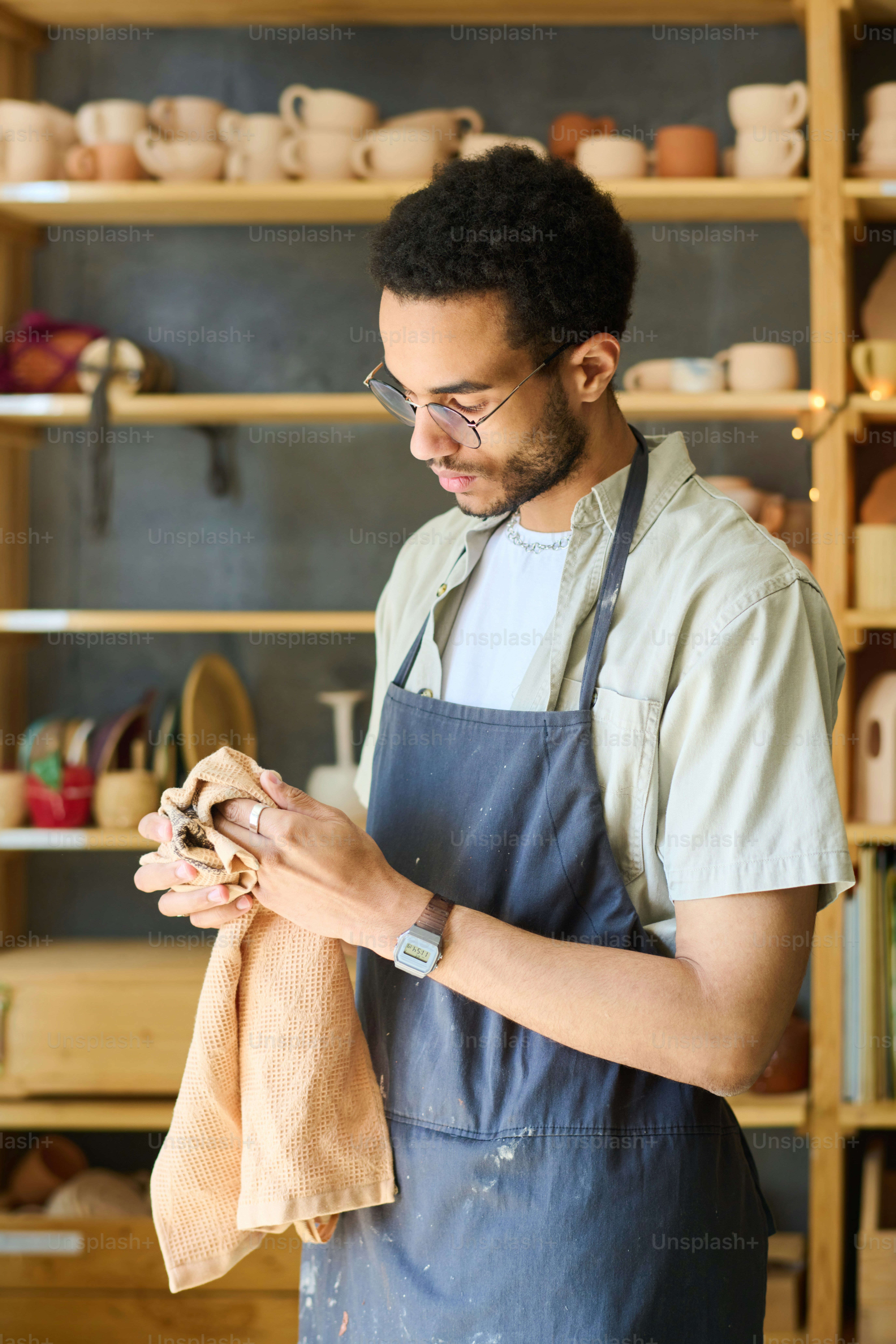 Young multi-ethnic craftsman in apron wiping his hands with towel while ...