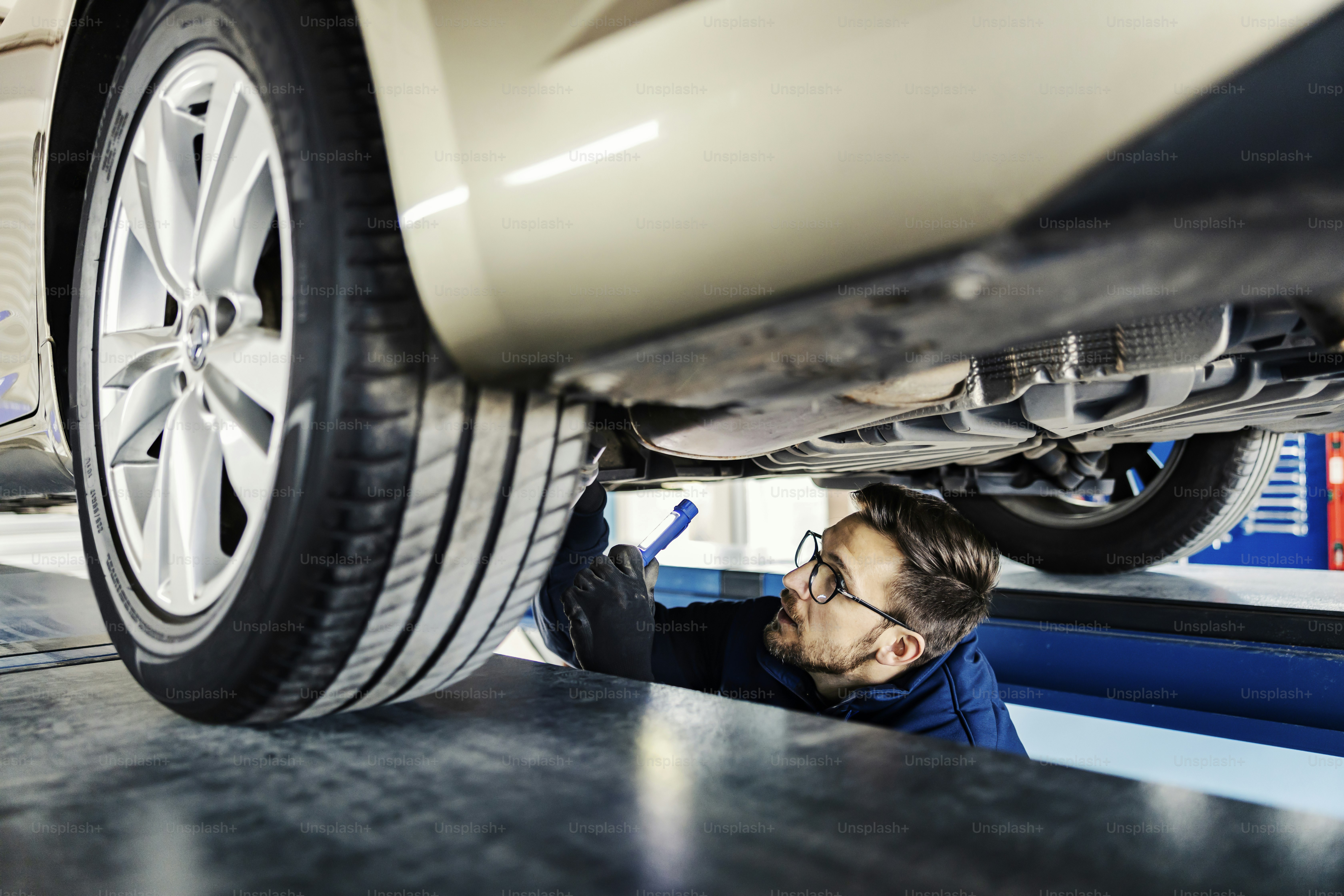 A technician examining auto in mechanic's pit. photo – Car wheel Image ...