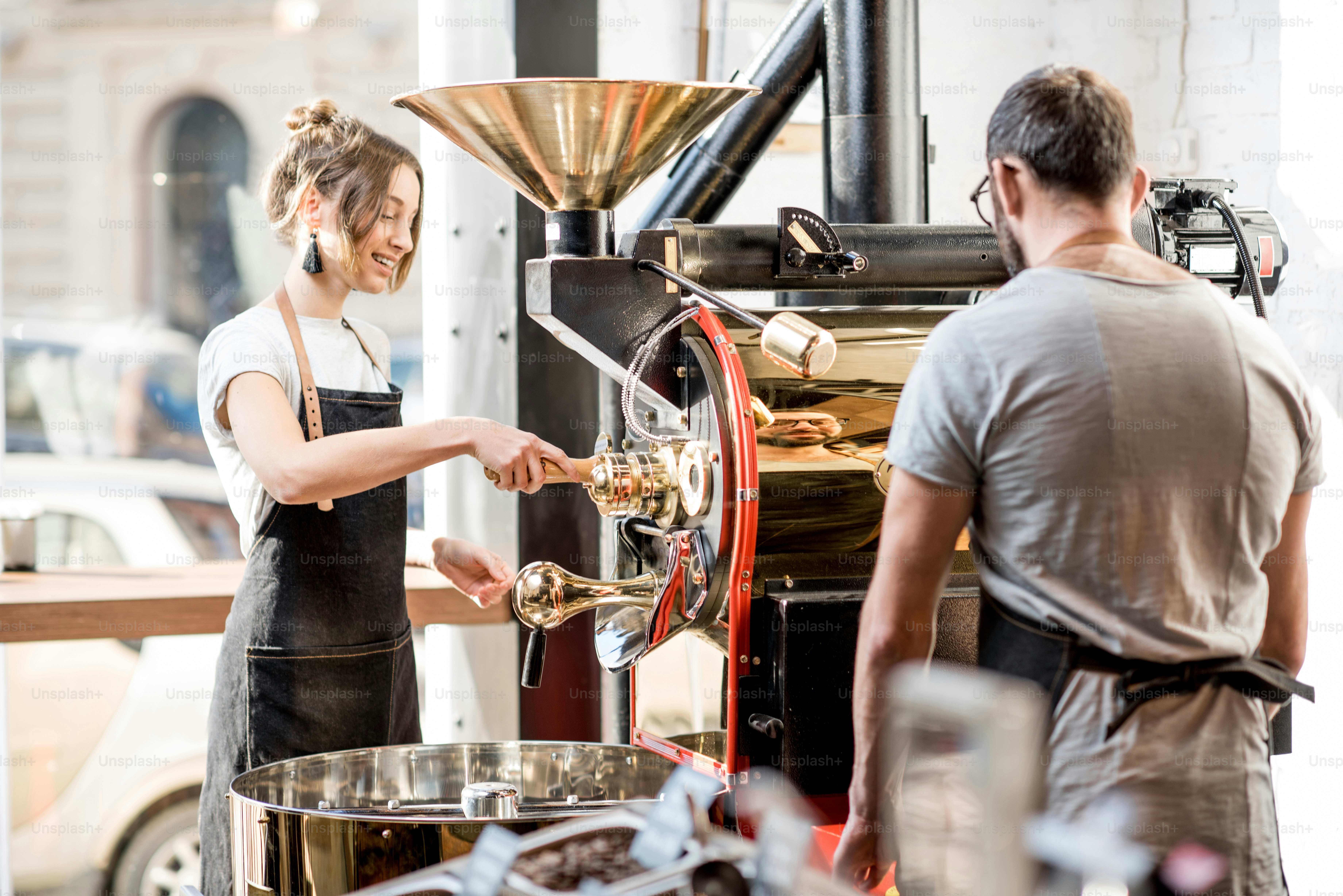 Man and woman in uniform working with roaster machine roasting coffee ...