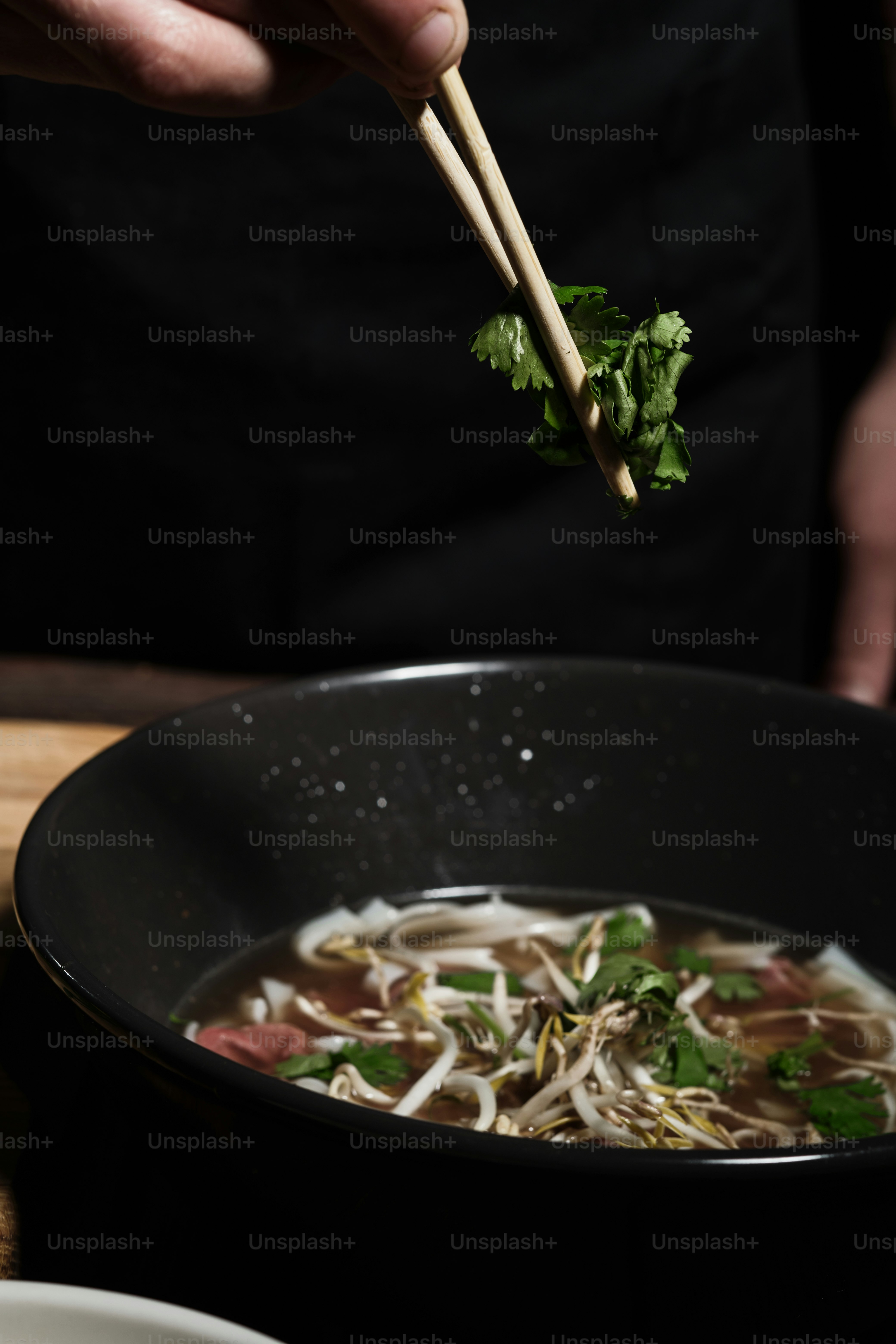 Close up of chef's hands grabbing parsley, adding to a bowl of pho bo ...