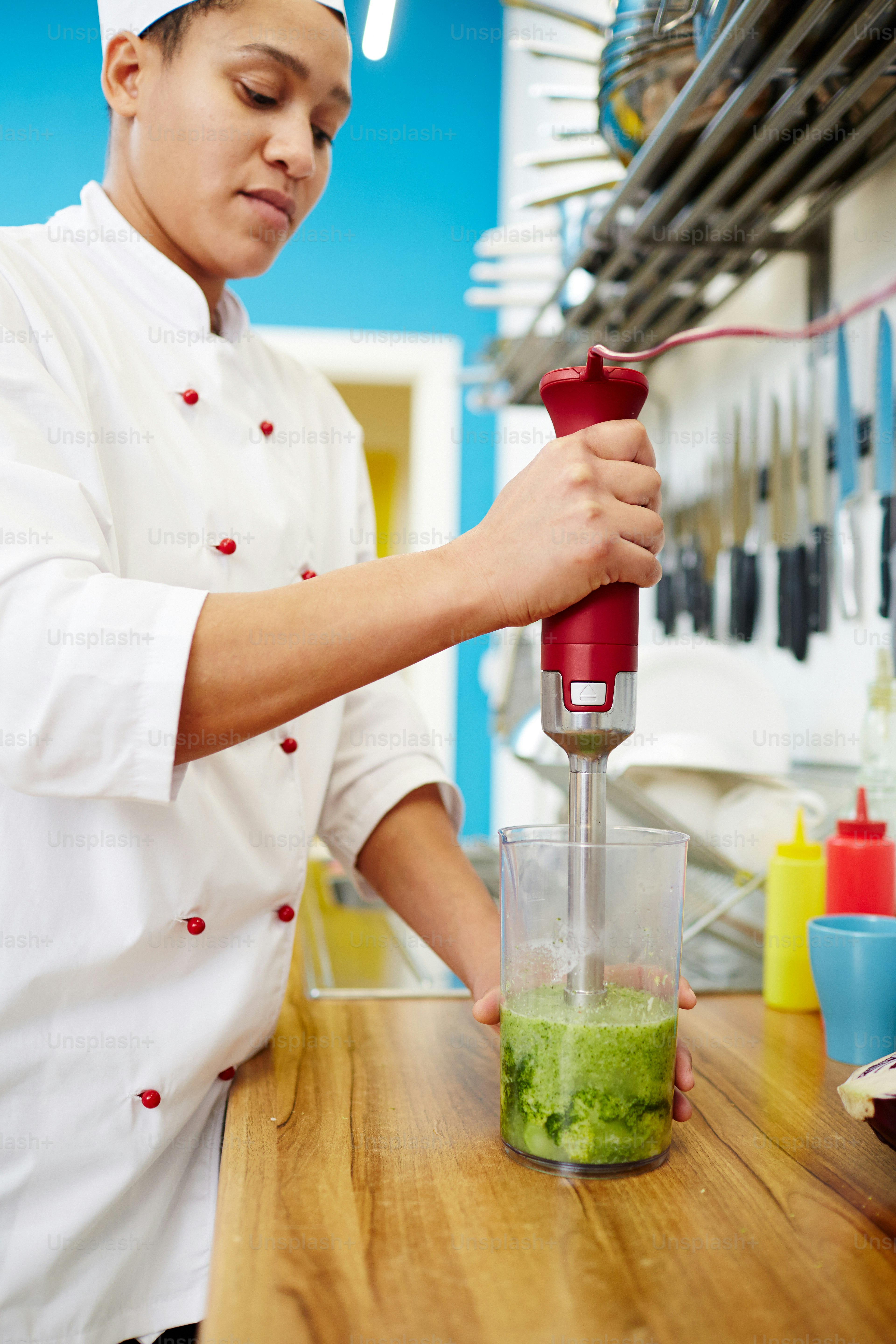 Woman in chef uniform blendering broccoli in plastic glass for cream ...