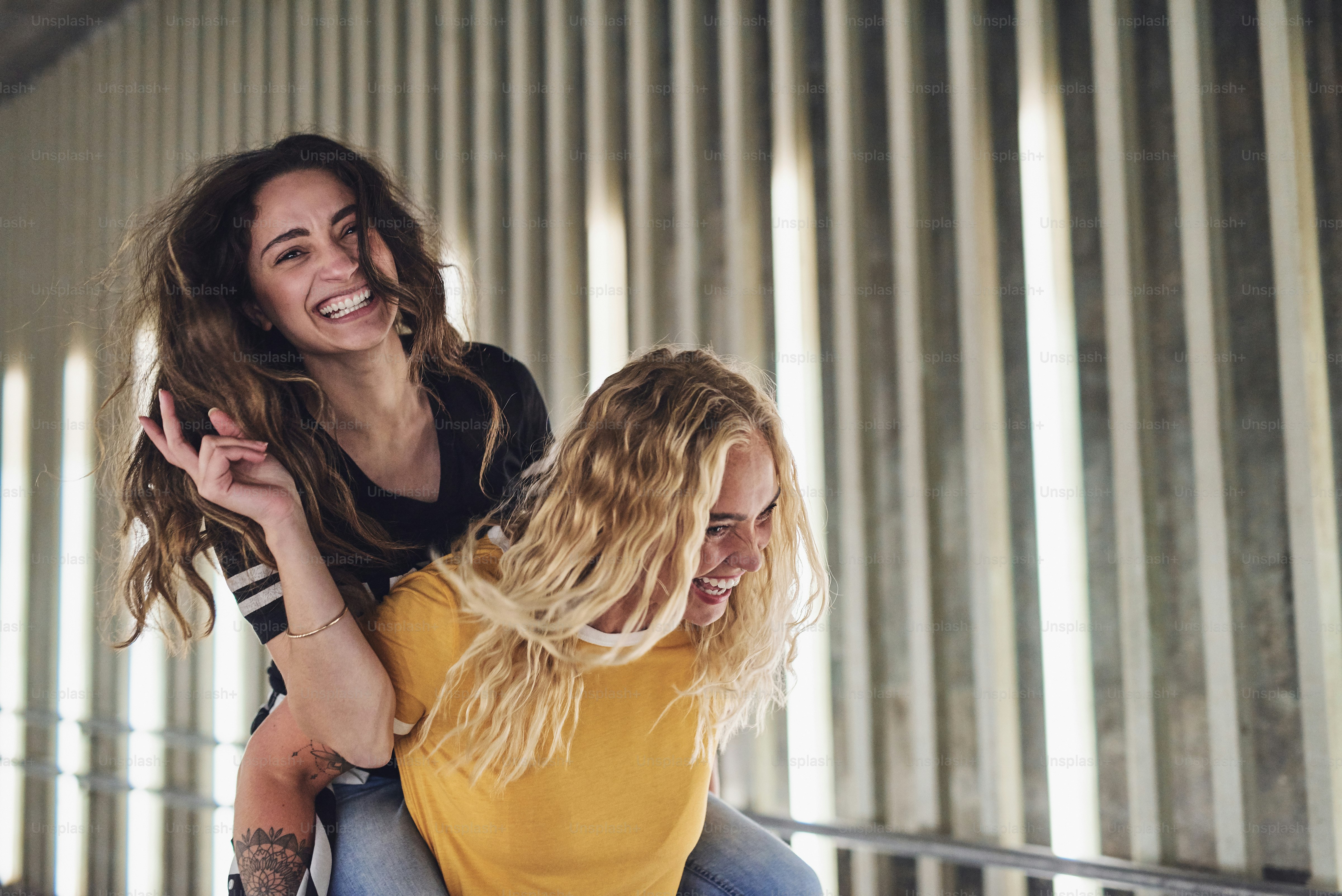 Laughing young woman being piggybacked by her friend while having a fun ...