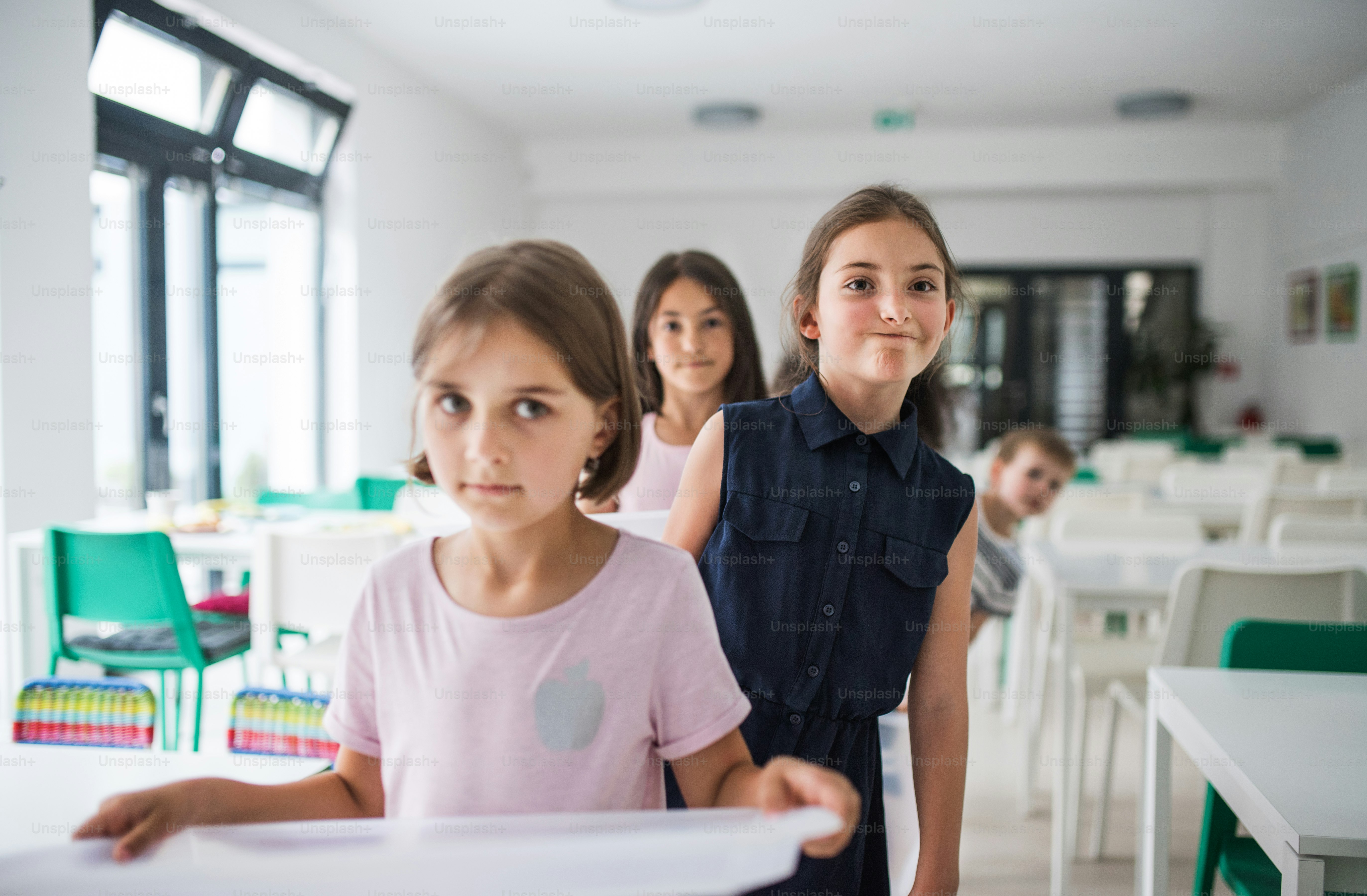 A group of cheerful small school kids with plastic trays in canteen ...