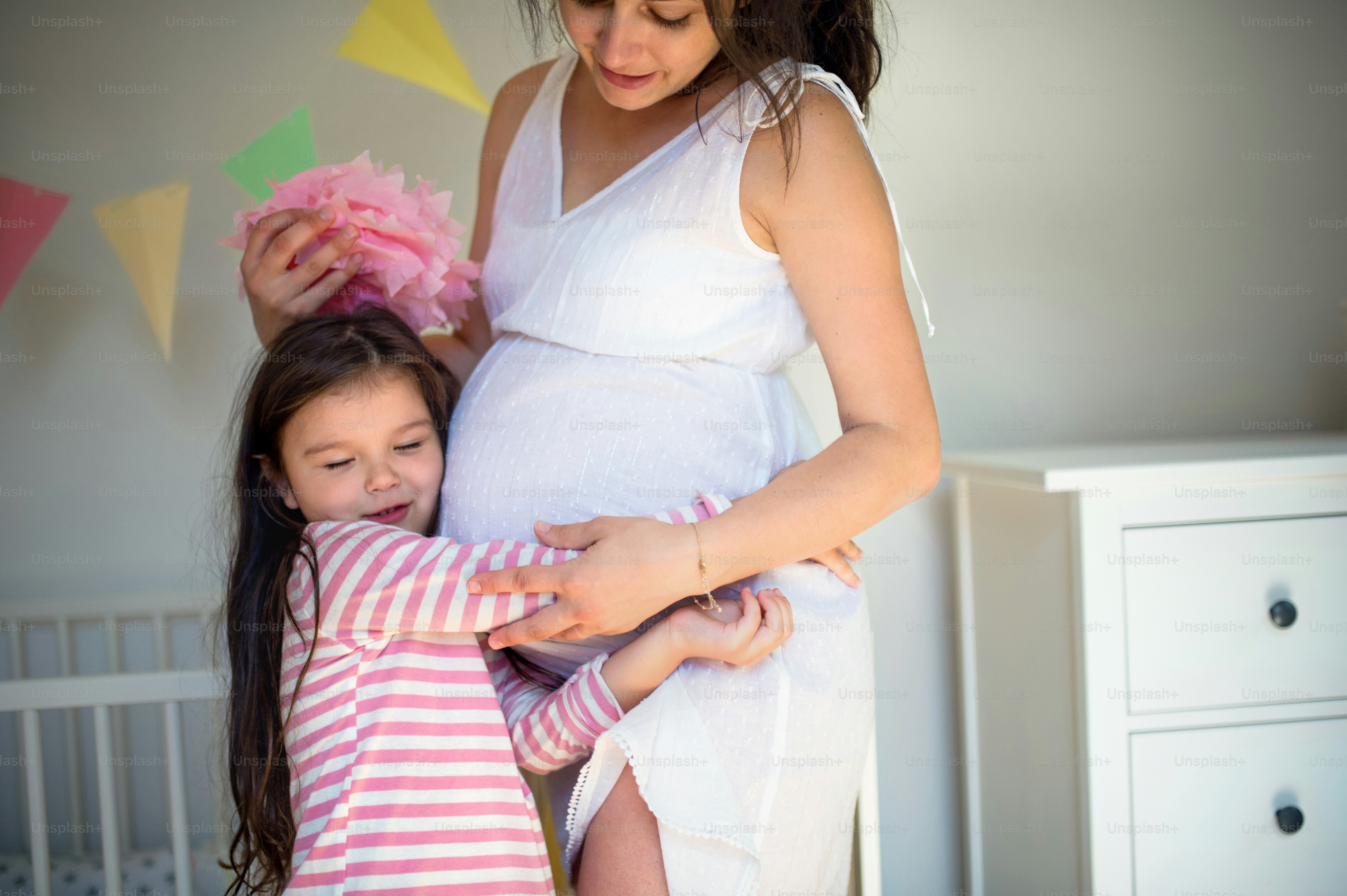 Portrait of pregnant woman with small daughter indoors at home, having ...