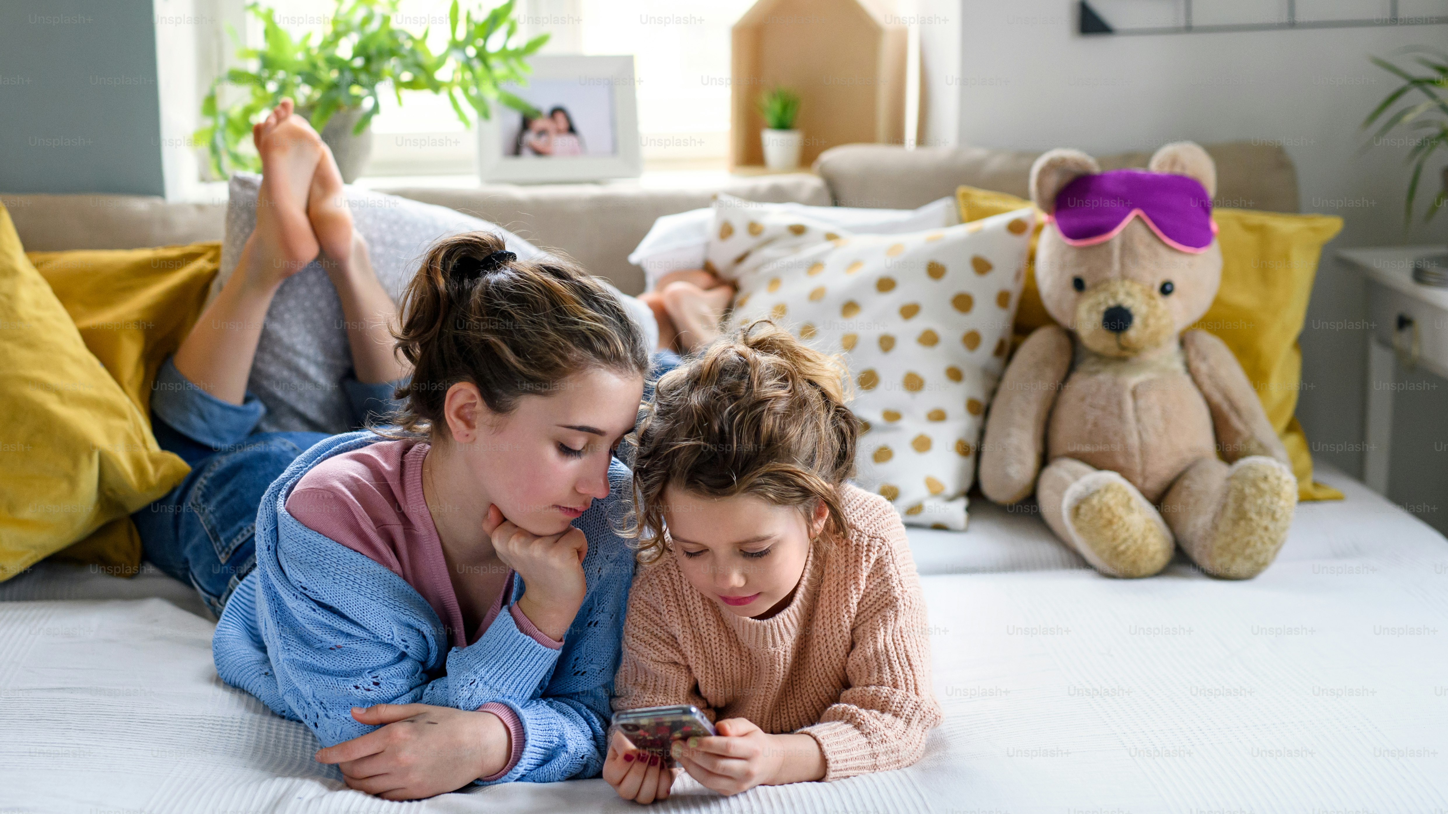 Portrait of sisters indoors at home, using smartphone. Lockdown concept ...