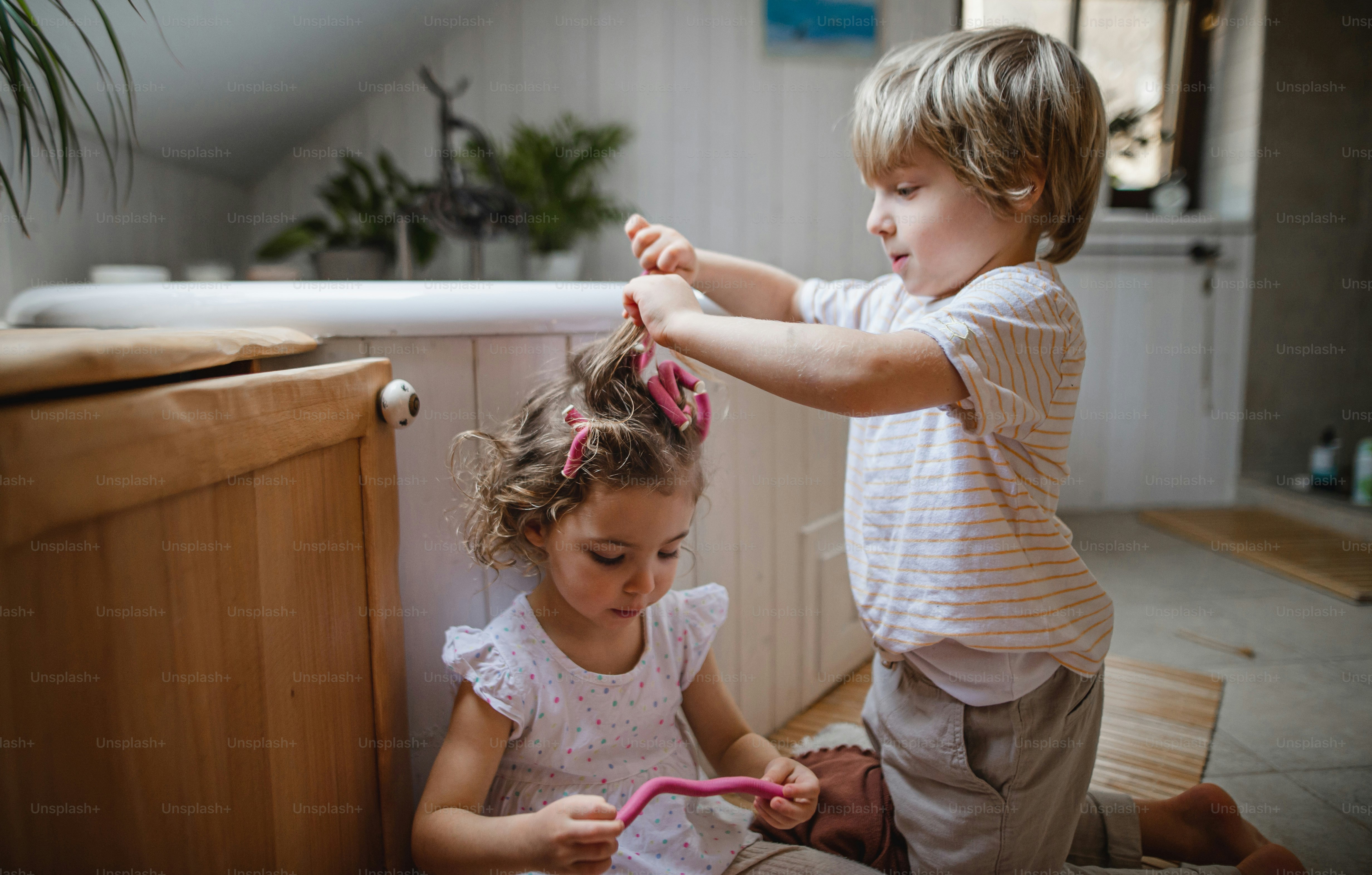 A little boy applying hair culers hair curlers to his little sister ...