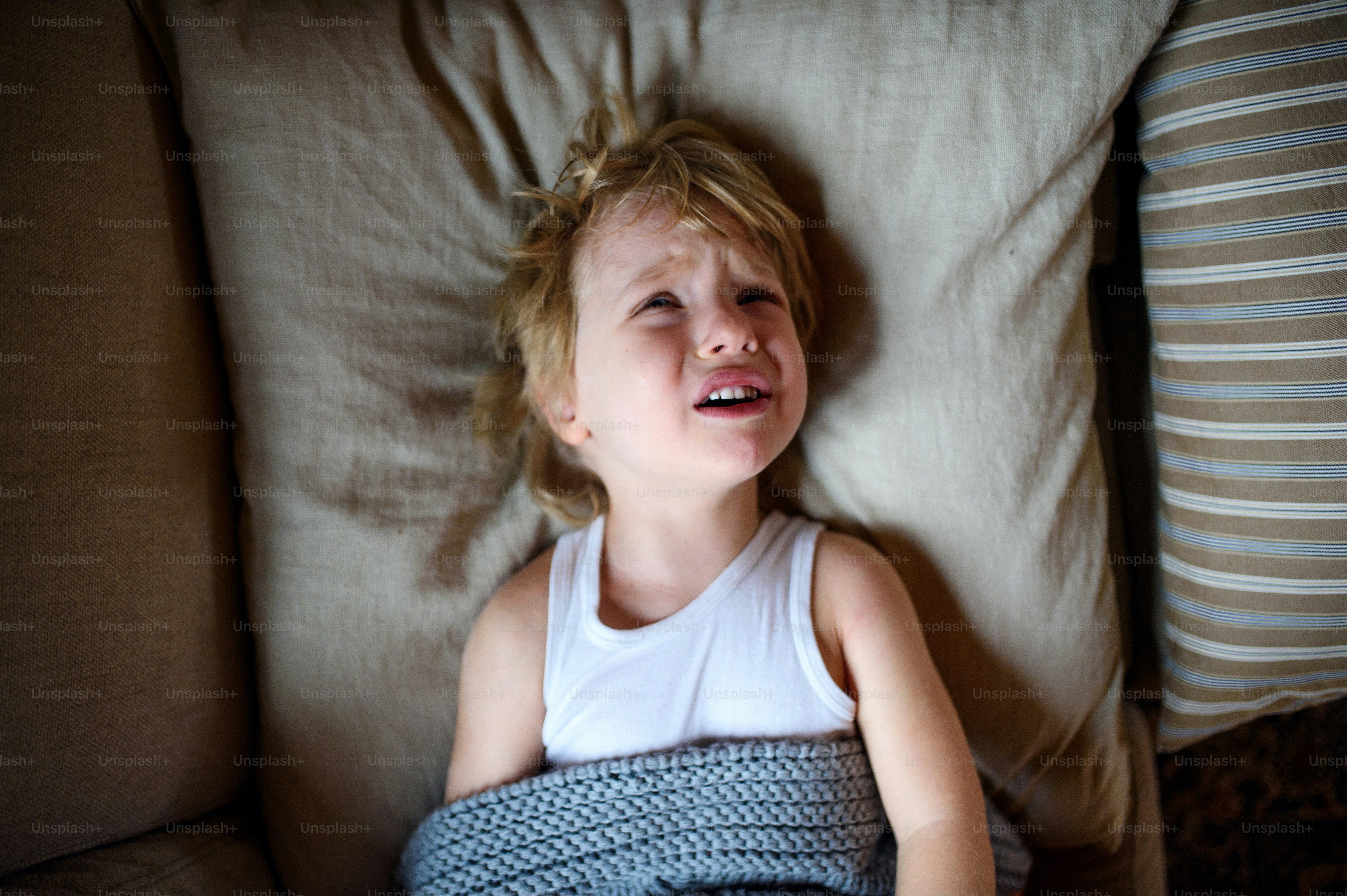 Top view of crying small sick boy lying in bed indoors at home. photo ...