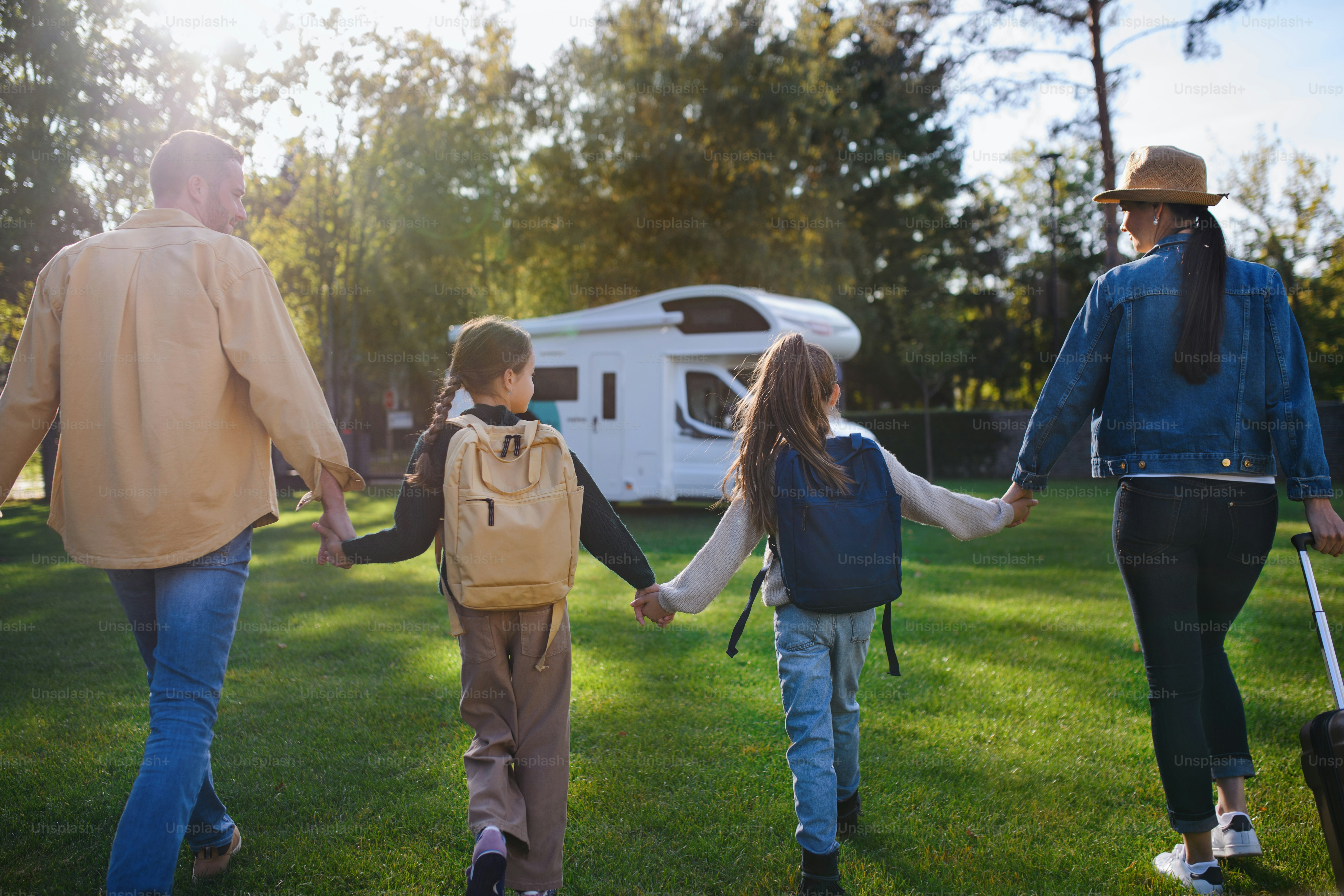 A rear view of young family with suitcases going to caravan outdoors at ...