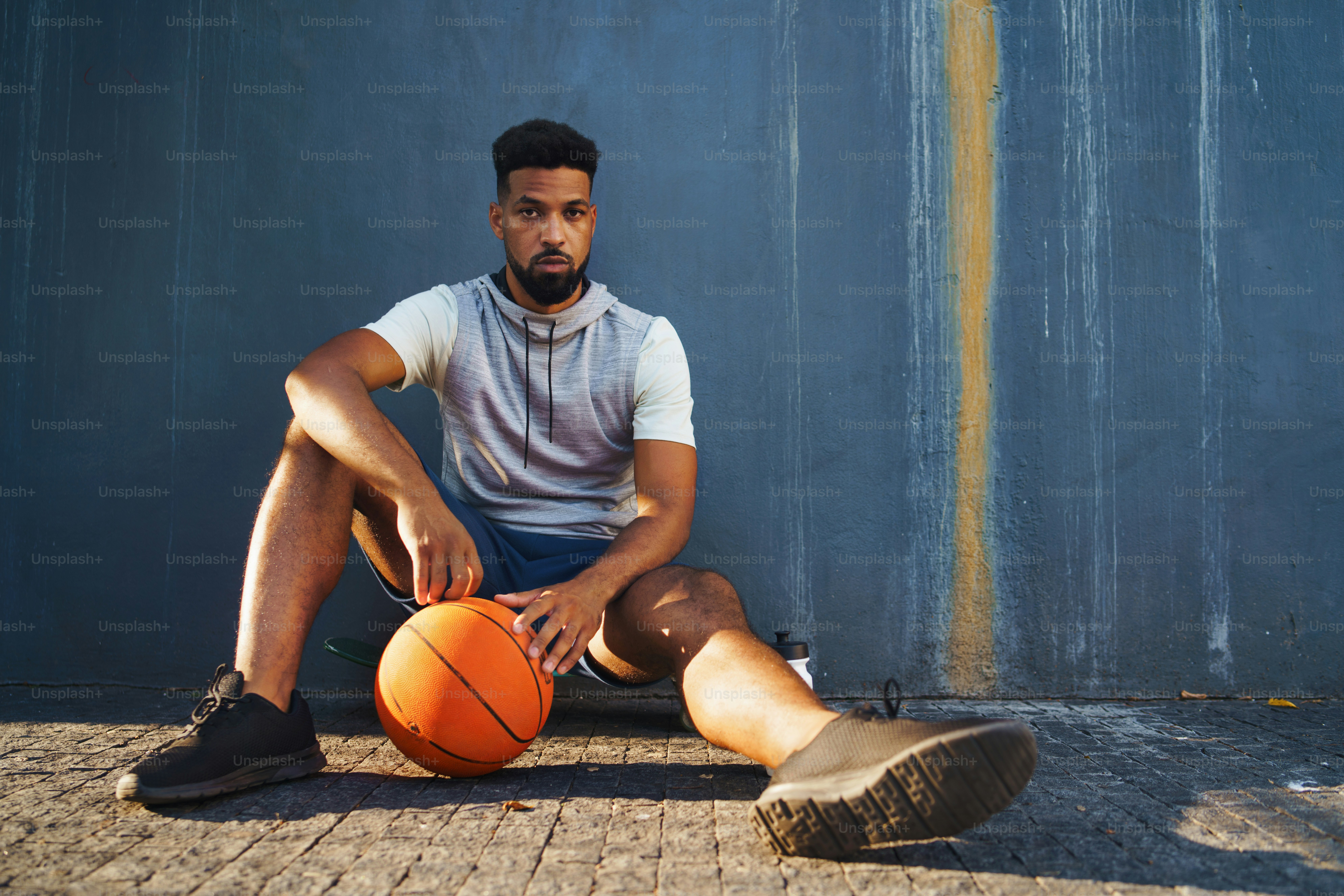 A young man with basketball doing exercise outdoors in city, sitting ...