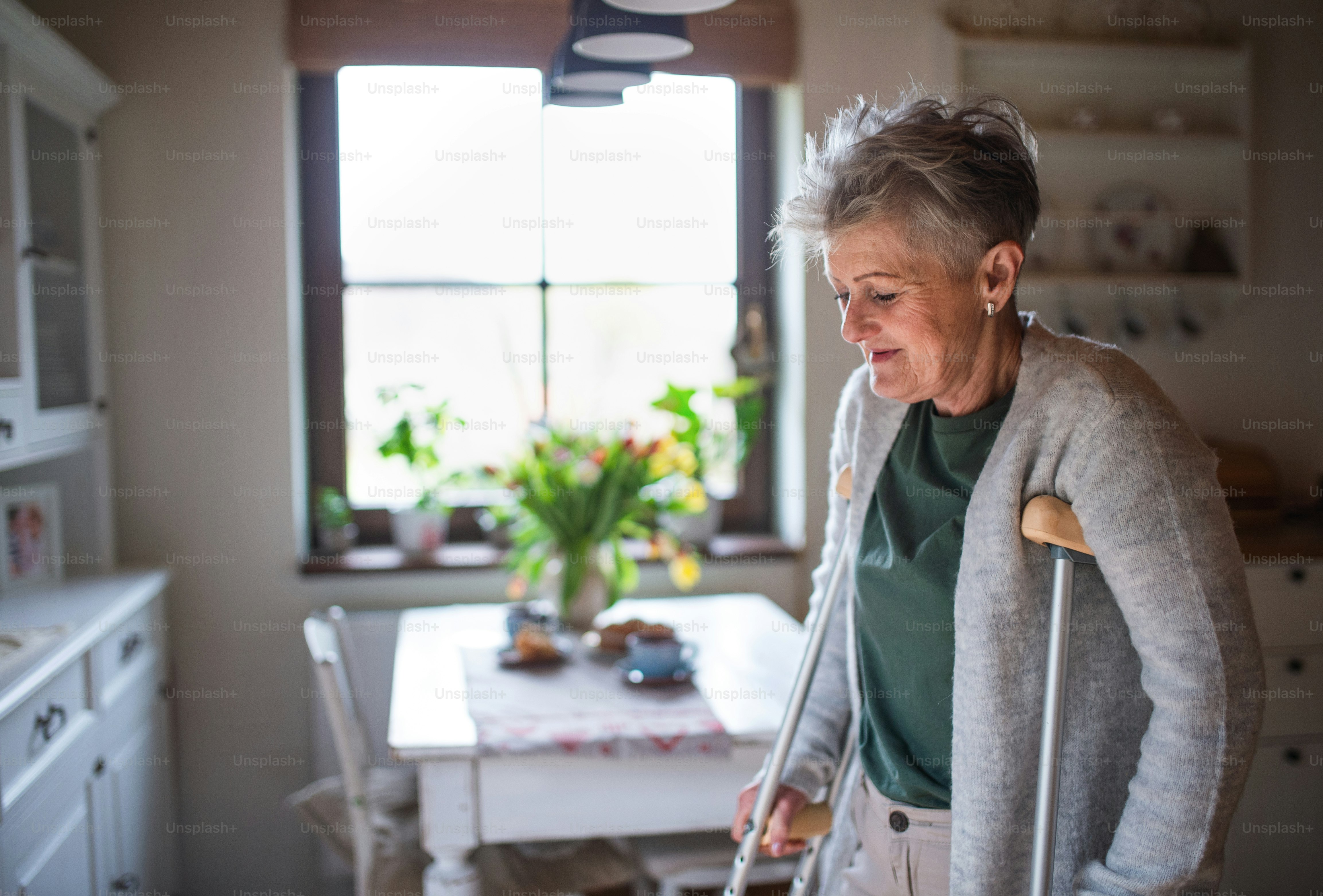 A ill senior mother with crutches indoors at home, walking. photo – Old ...
