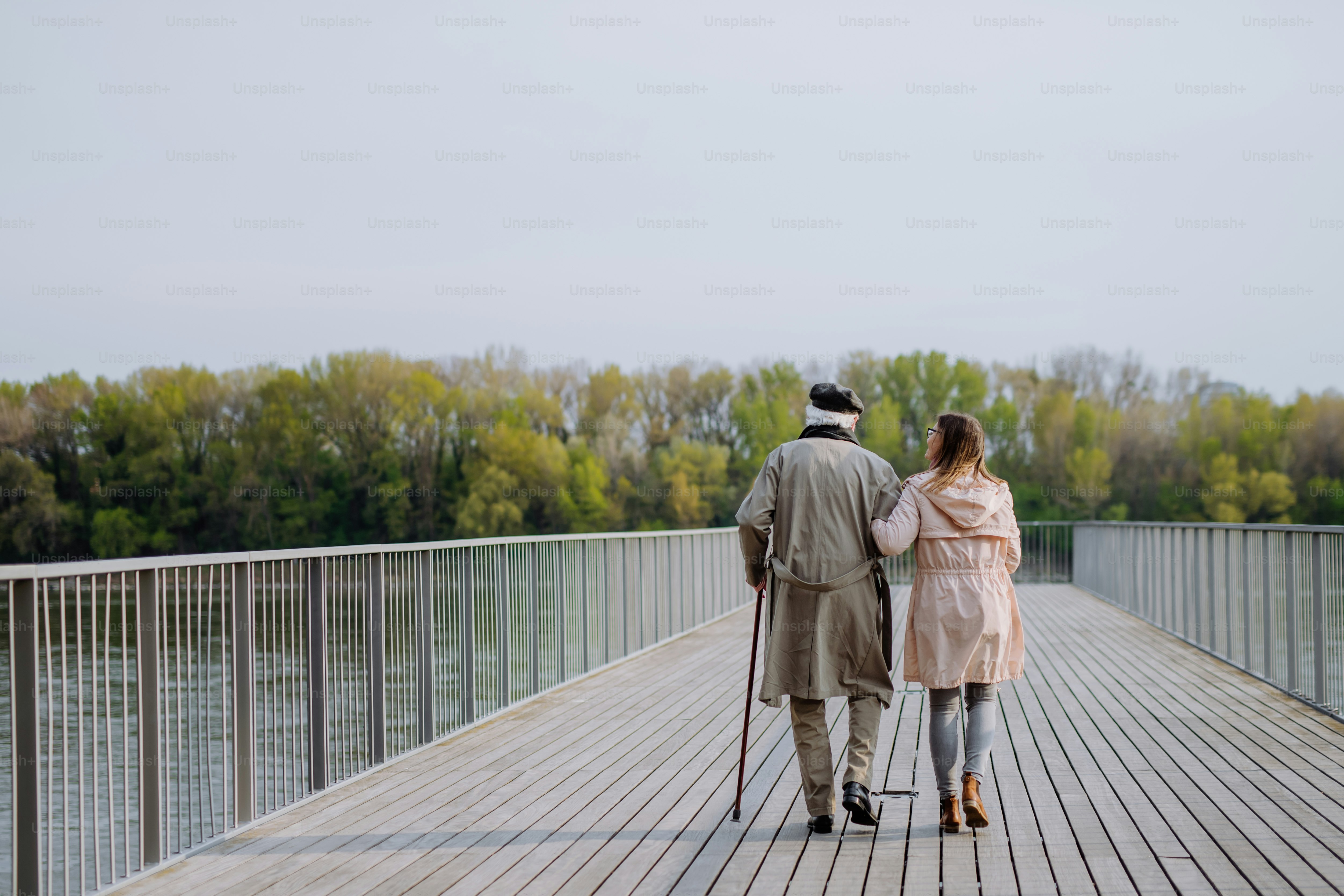A rear view of senior man with daughter outdoors on a walk on pier by ...