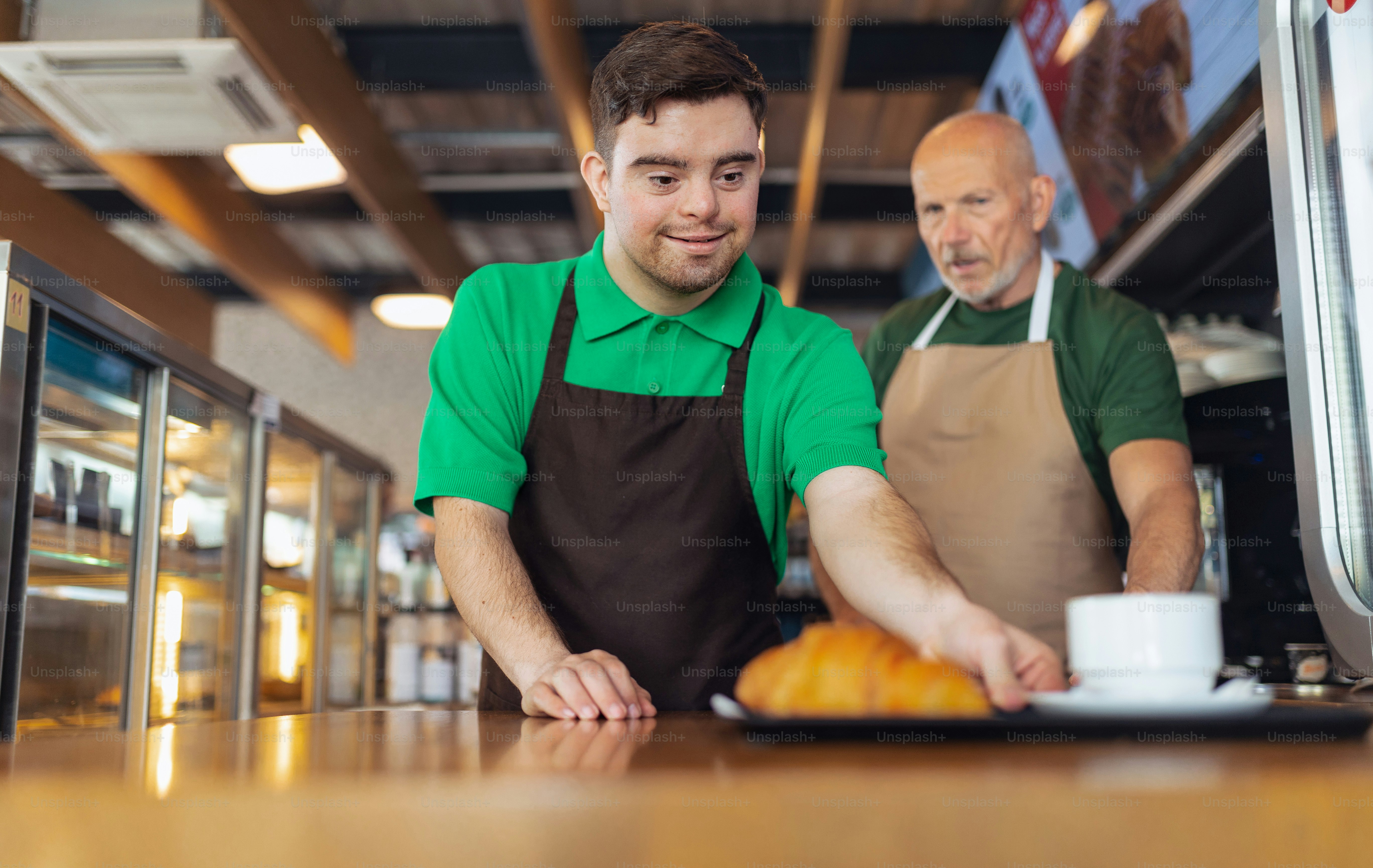 A happy waiter with Down syndrome serving coffee with help of his ...