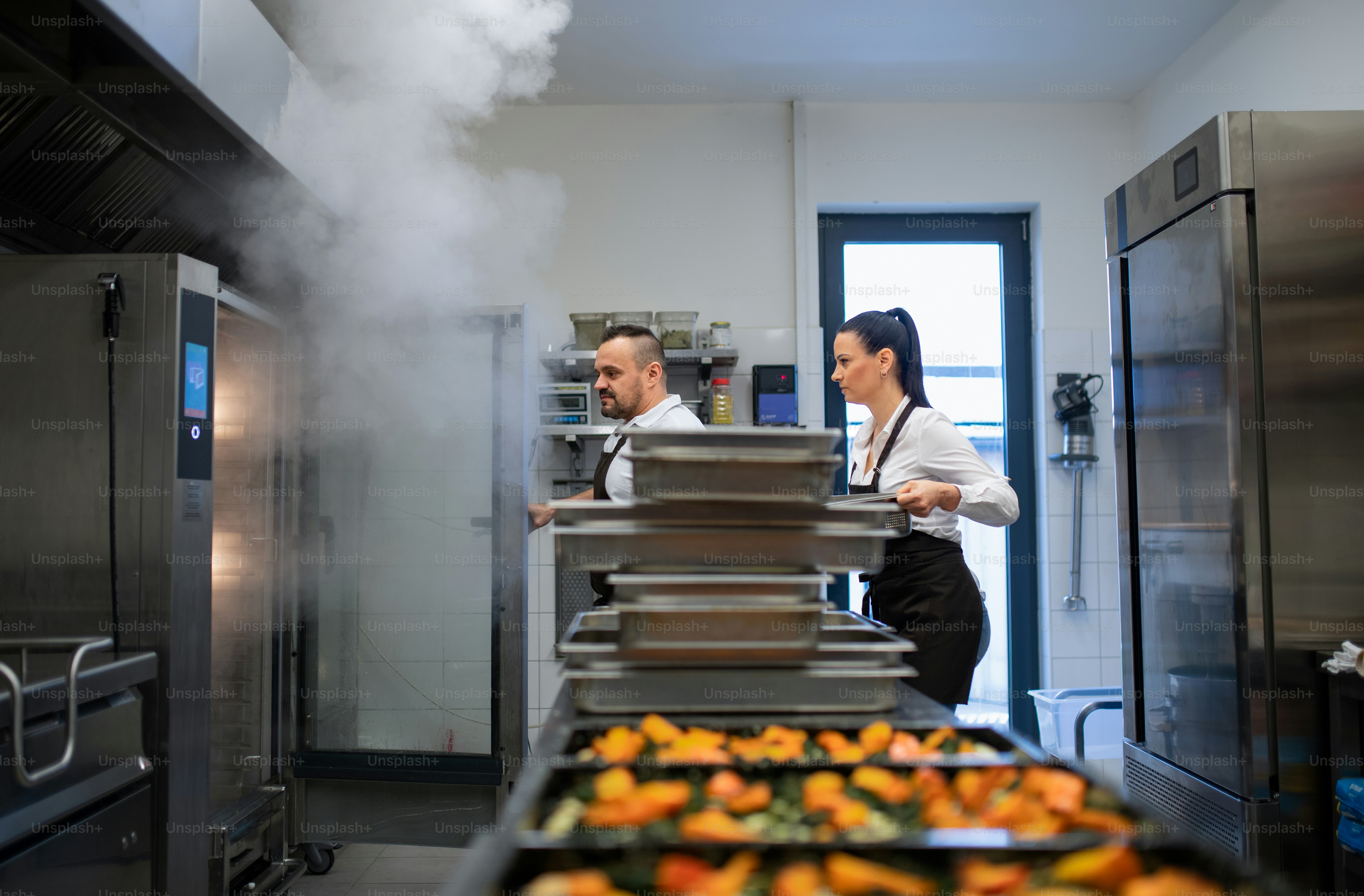 A chef and cook working on their dishes indoors in restaurant kitchen ...