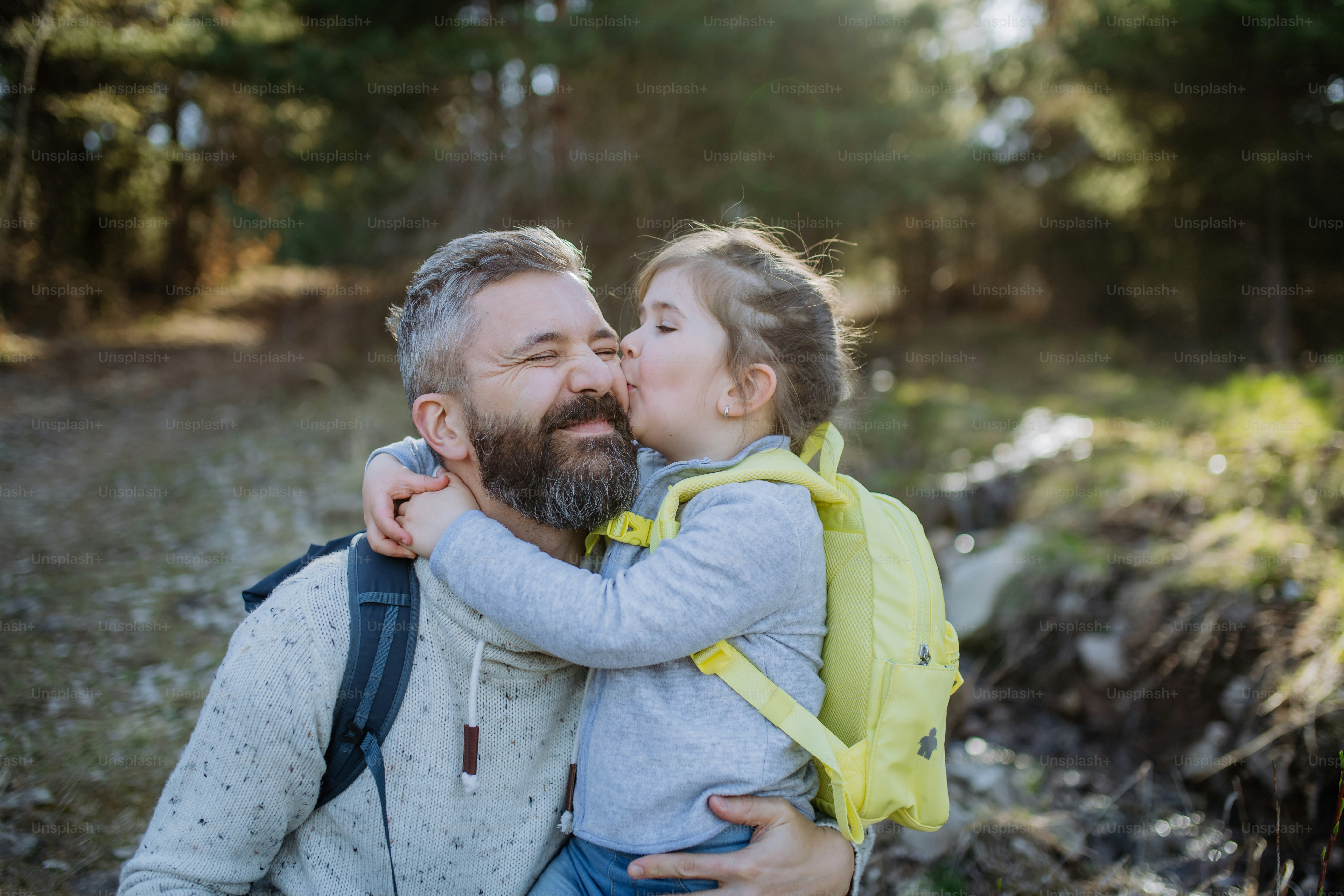 A little daughter kissing her father during walk in spring nature ...