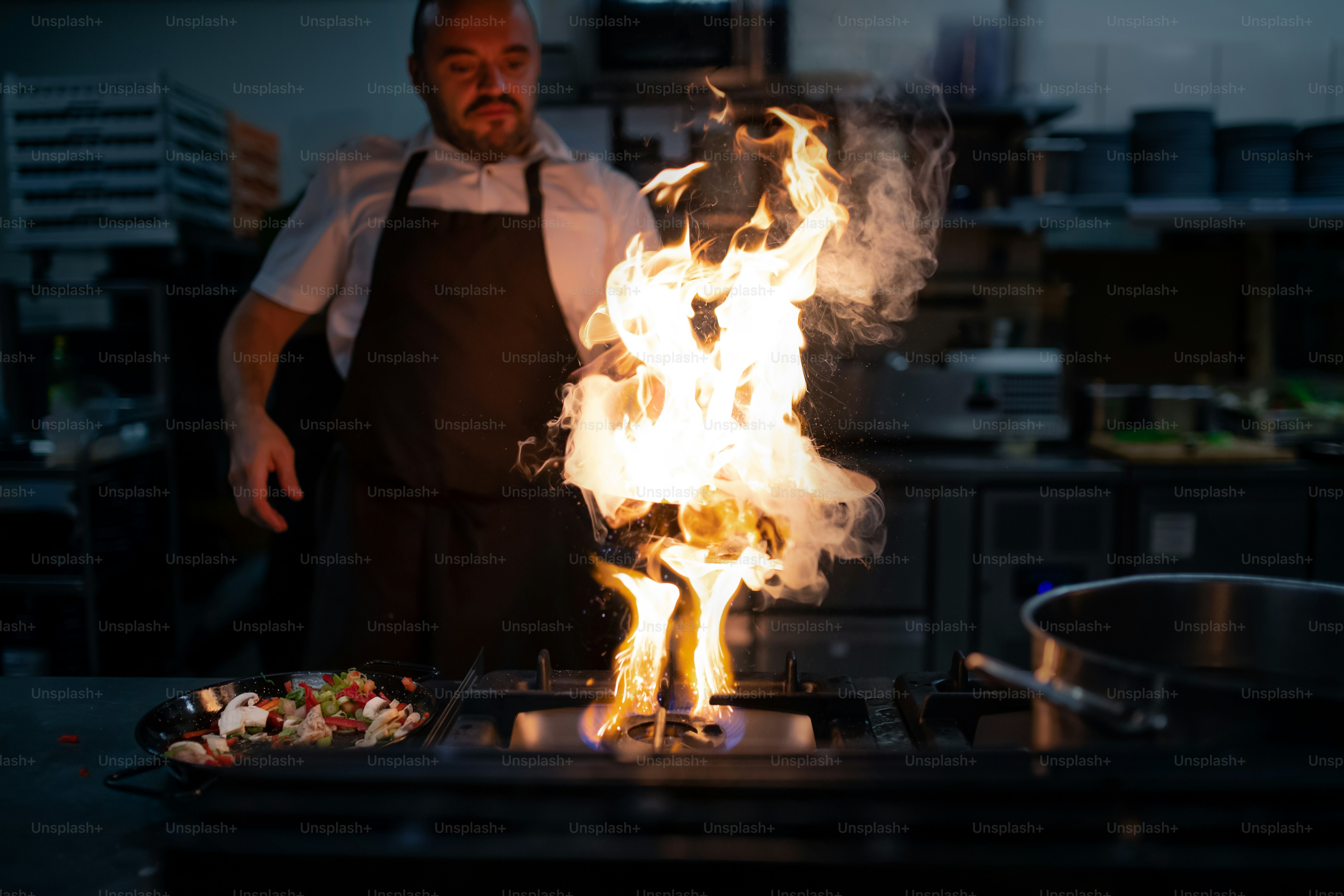 A professional chef preparing meal, flambing indoors in restaurant ...