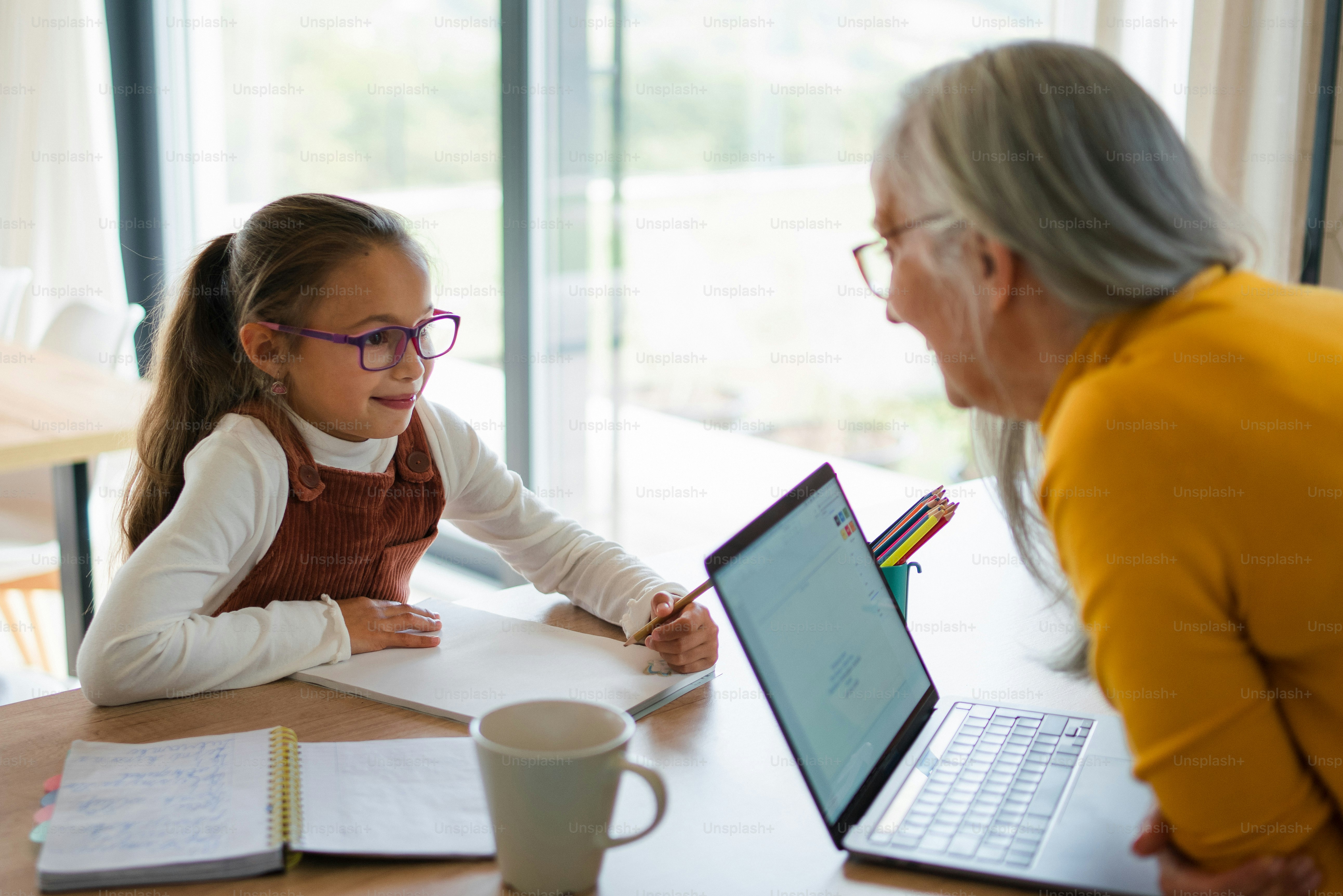 A small girl with senior grandmother doing homework at home. photo ...