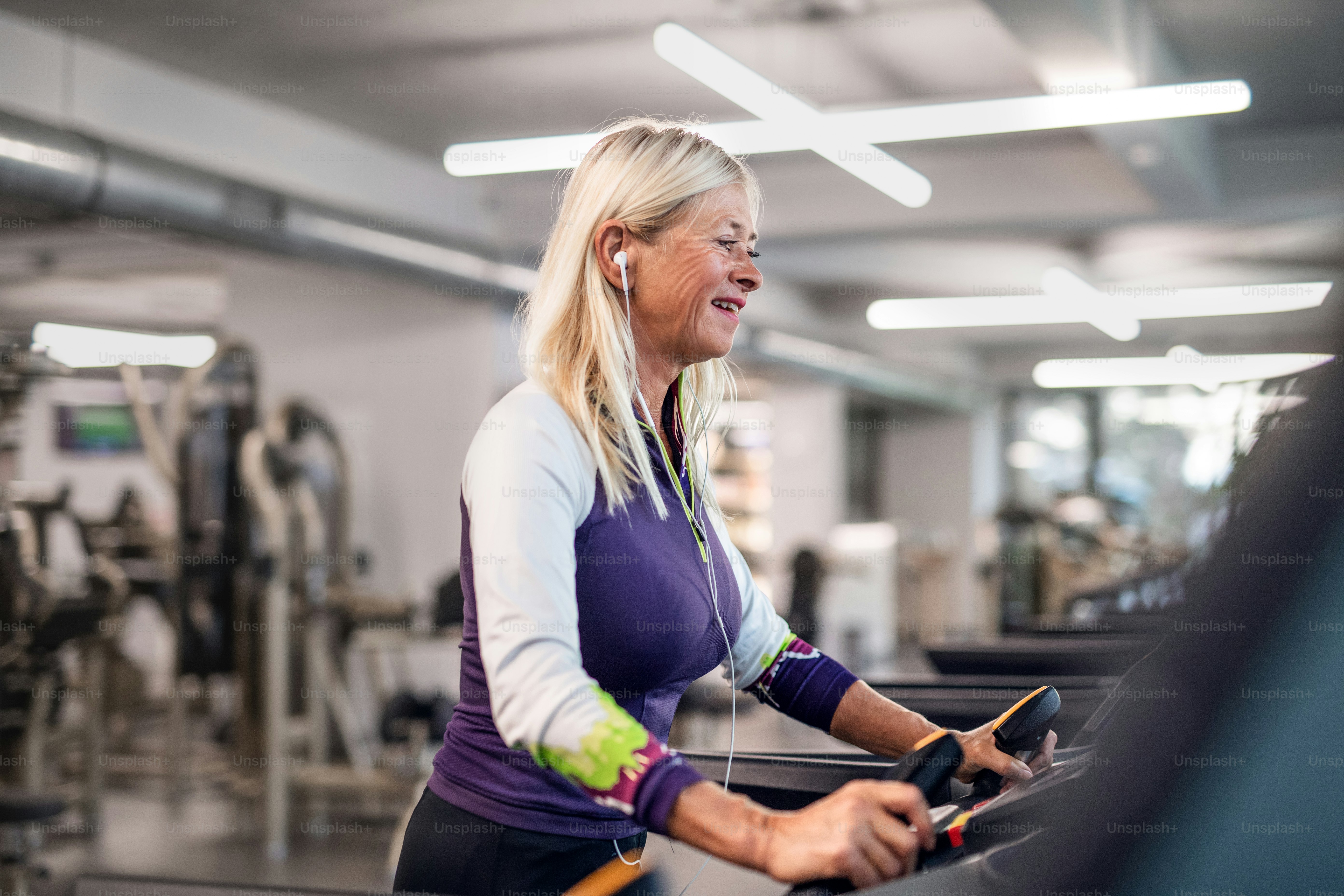 A happy senior woman with earphones in gym doing cardio work out ...