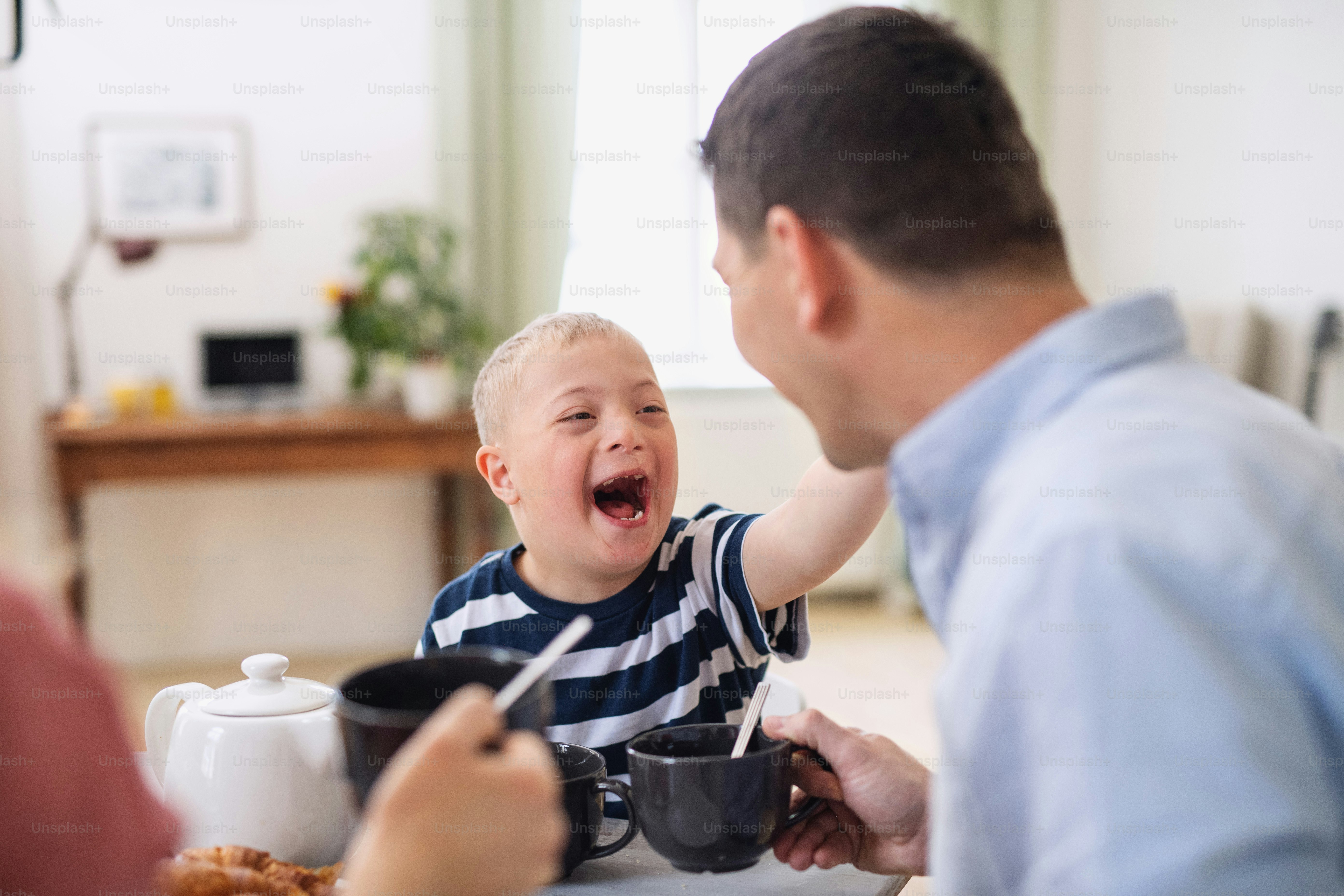A happy family with down syndrome son at the table, laughing when ...