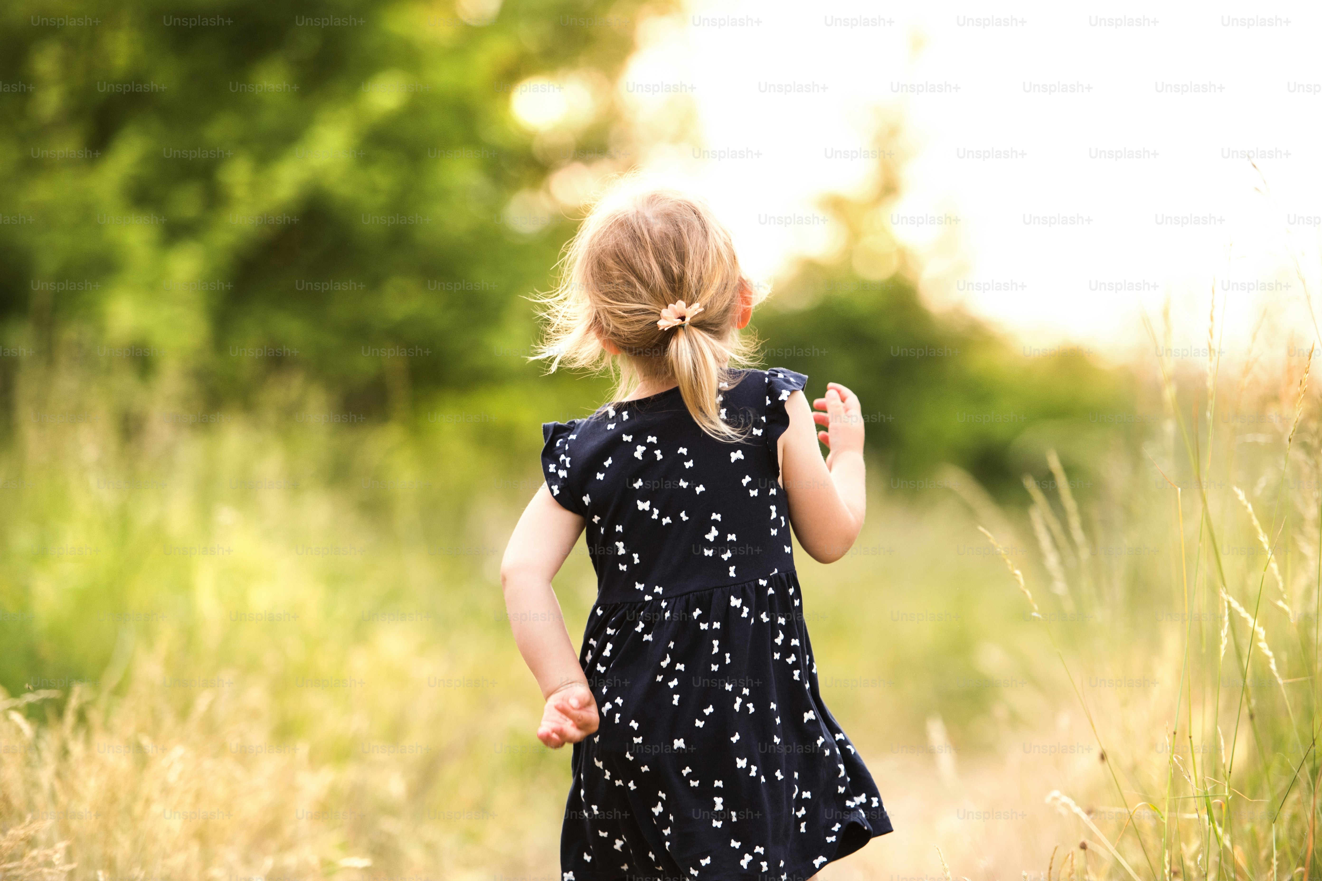 Cute little blonde girl in blue dress outside in in green sunny summer ...