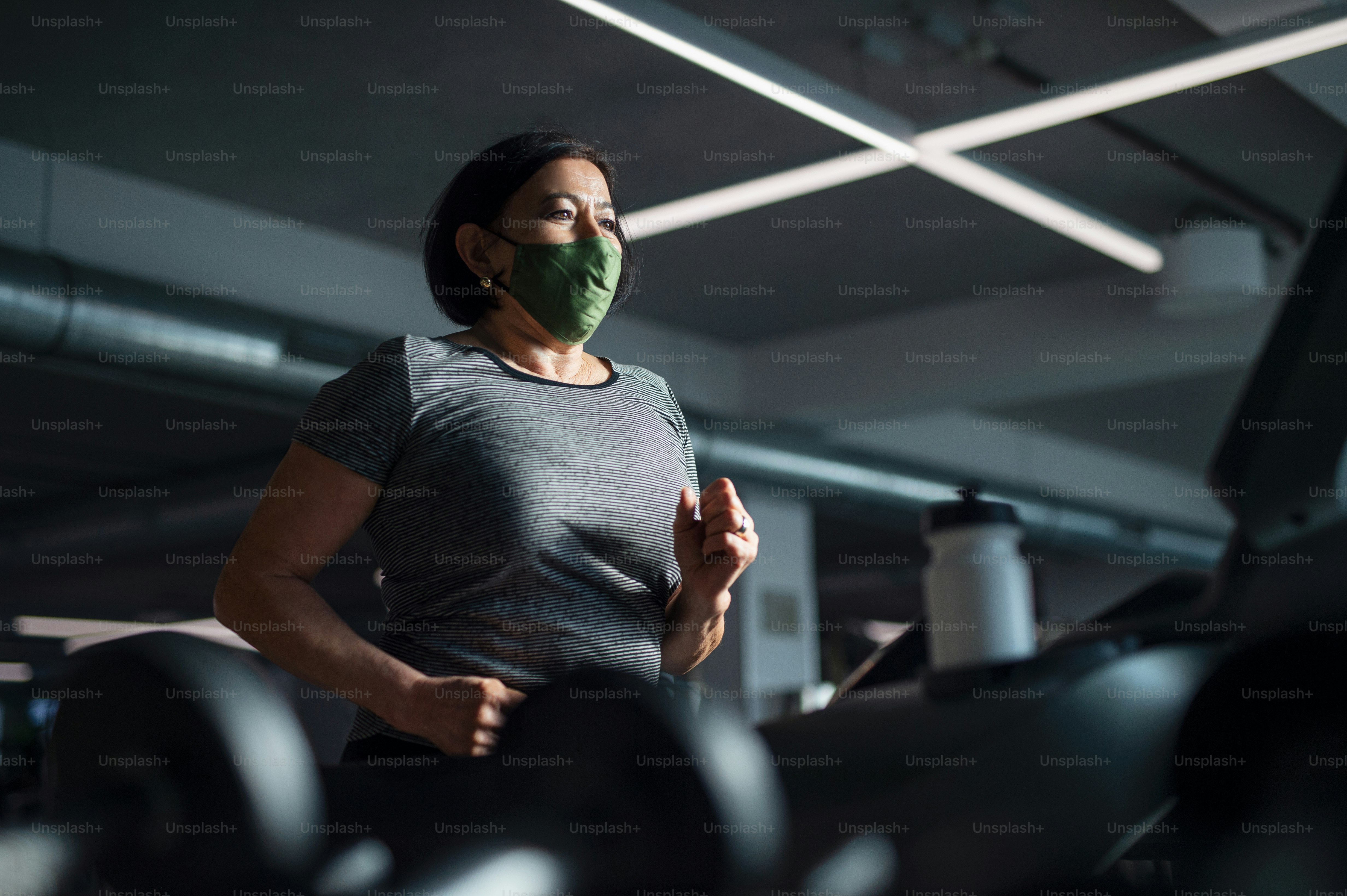 Side view of senior woman with face mask doing exercise on treadmill in ...