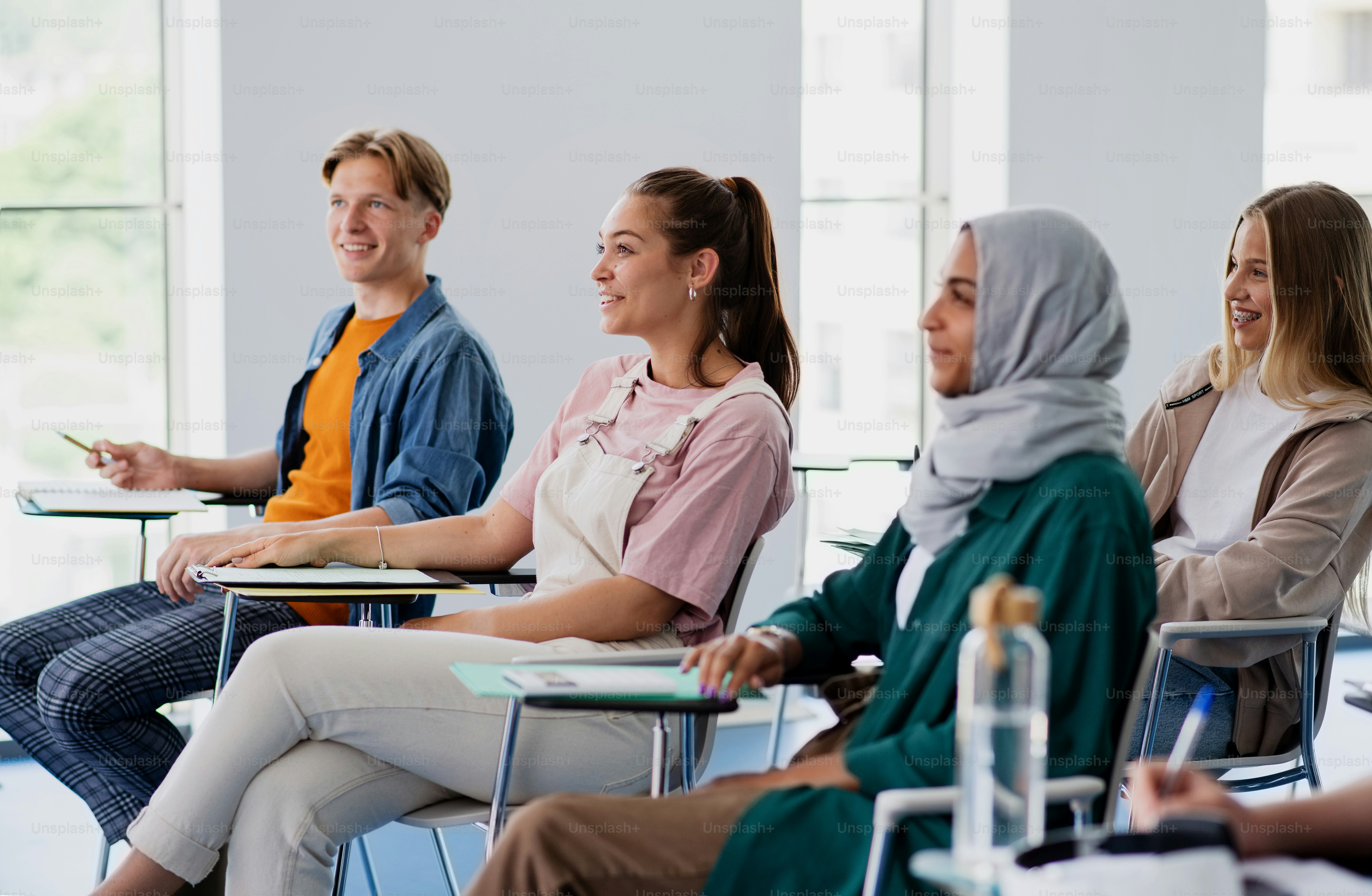 A group of multiethnic university students sitting in classroom indoors ...