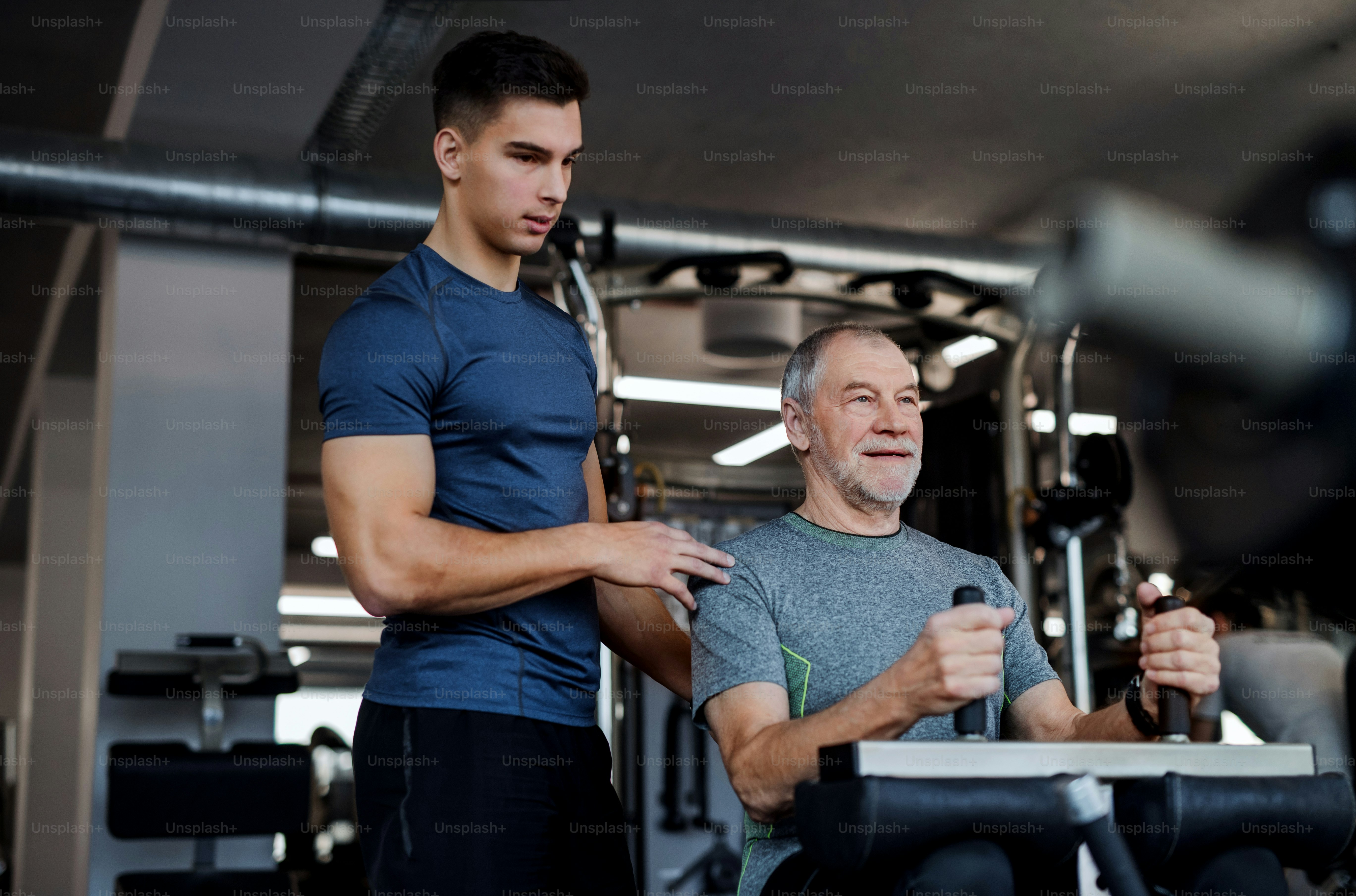 A senior man with a young male trainer doing strength workout exercise ...